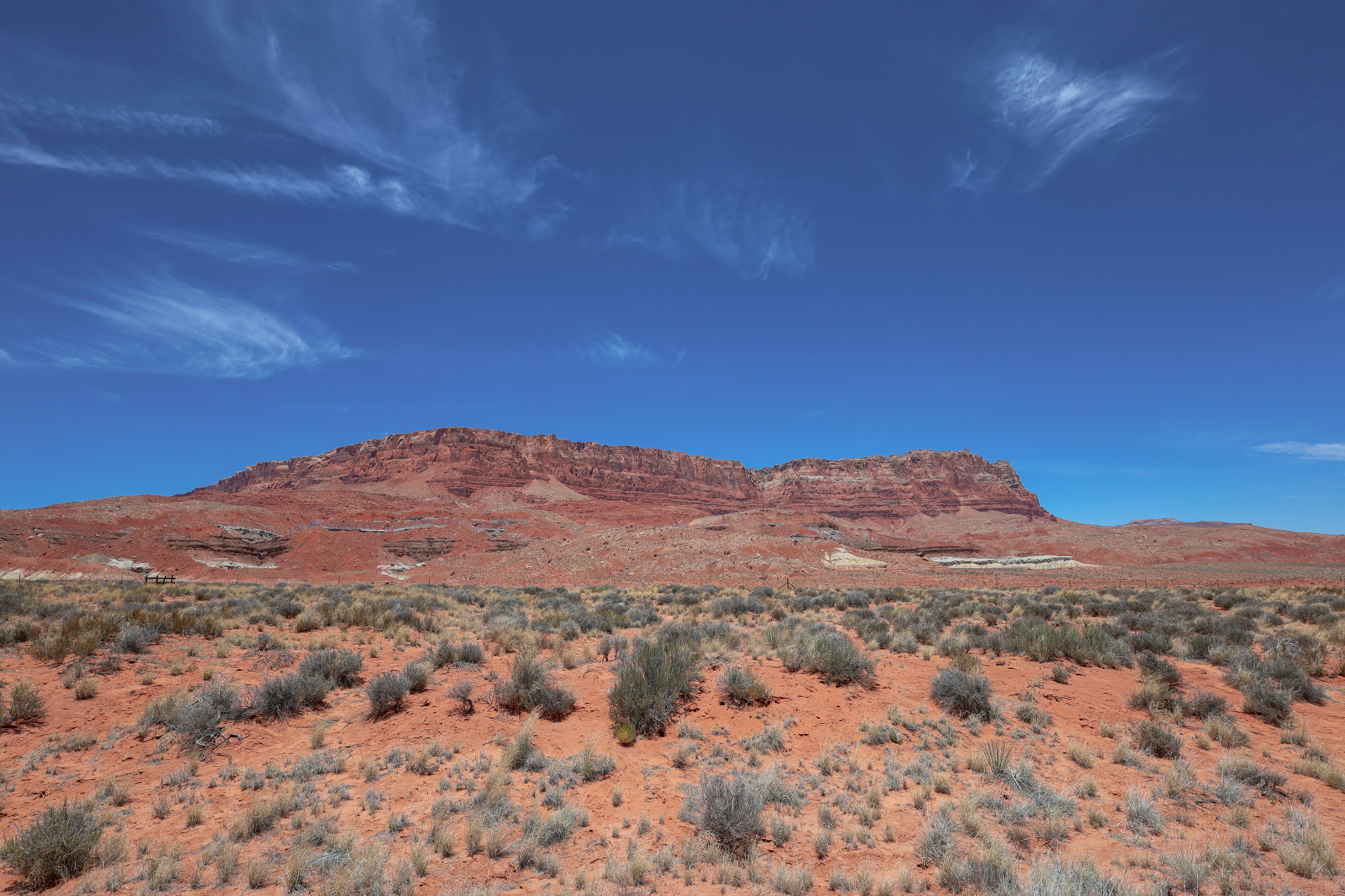 Expansive red desert landscape with a striking mesa under a vivid blue sky.