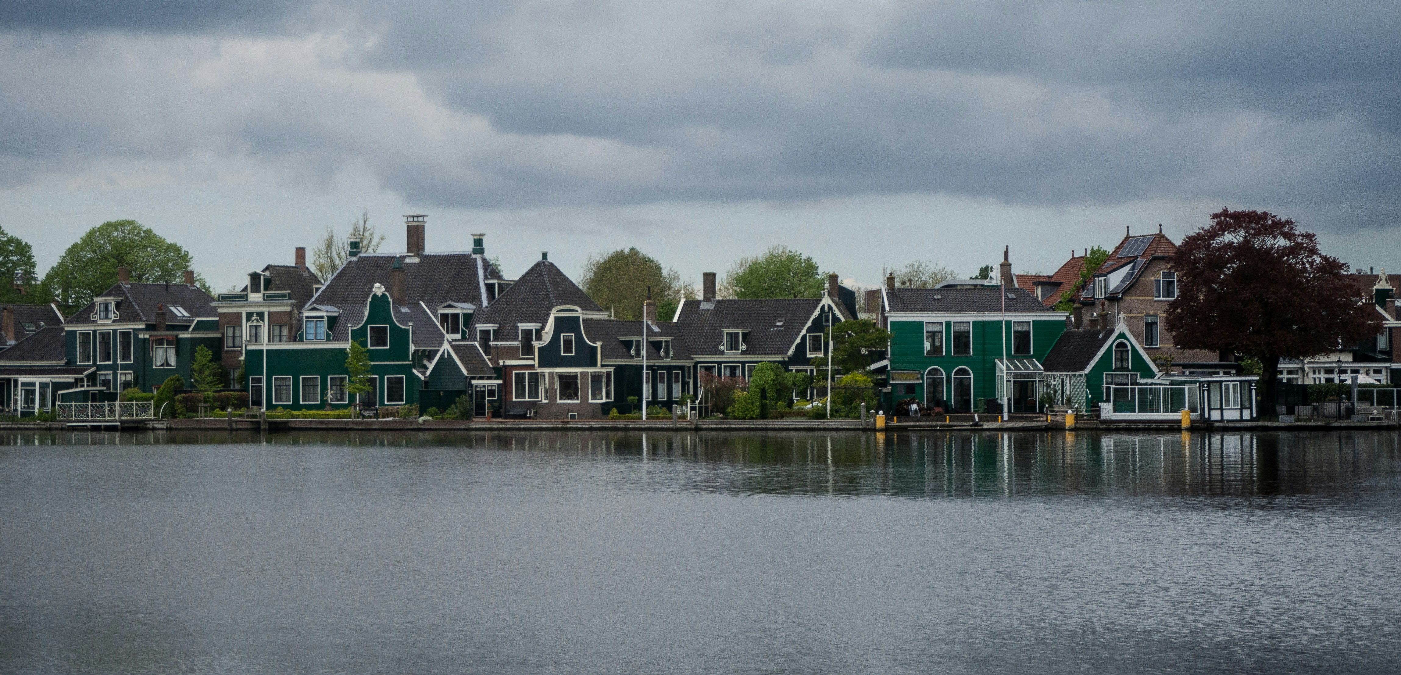 Charming green houses line the tranquil waterside, reflecting the rich architectural heritage against a moody sky.