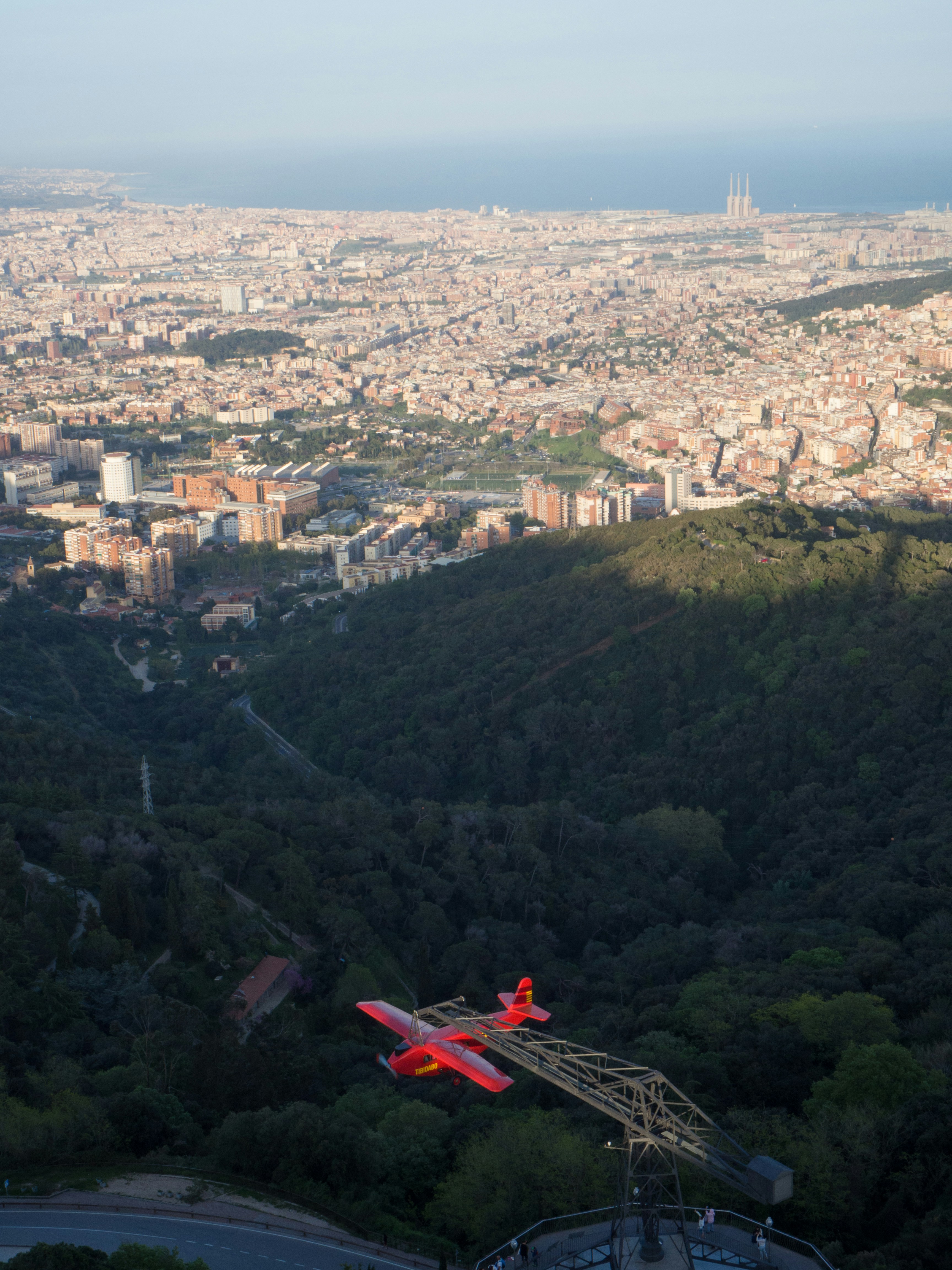 City Below the Crest: A Red-winged Plane Gliding Over Green Hills