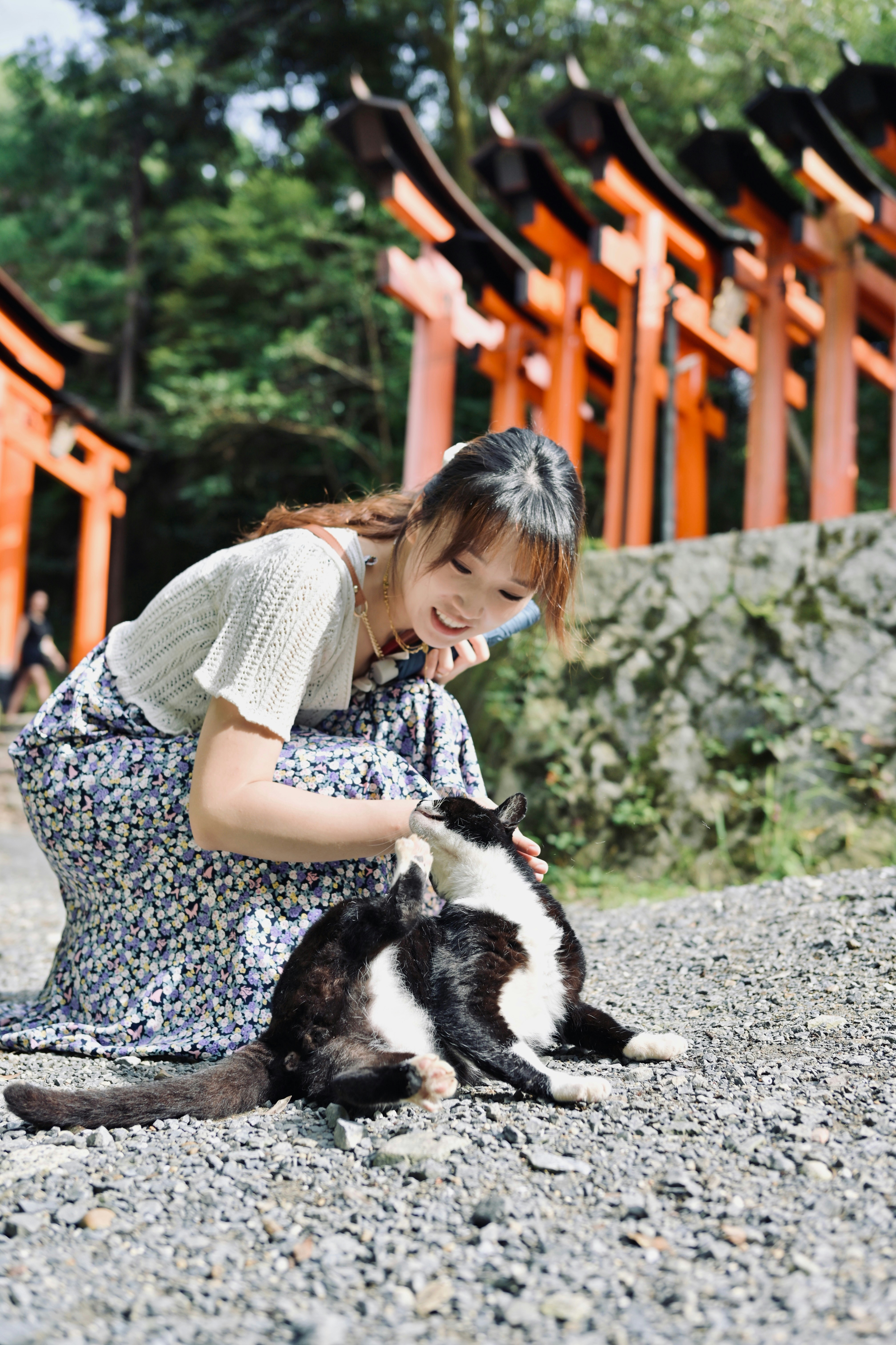 A woman petting a black and white cat on the ground