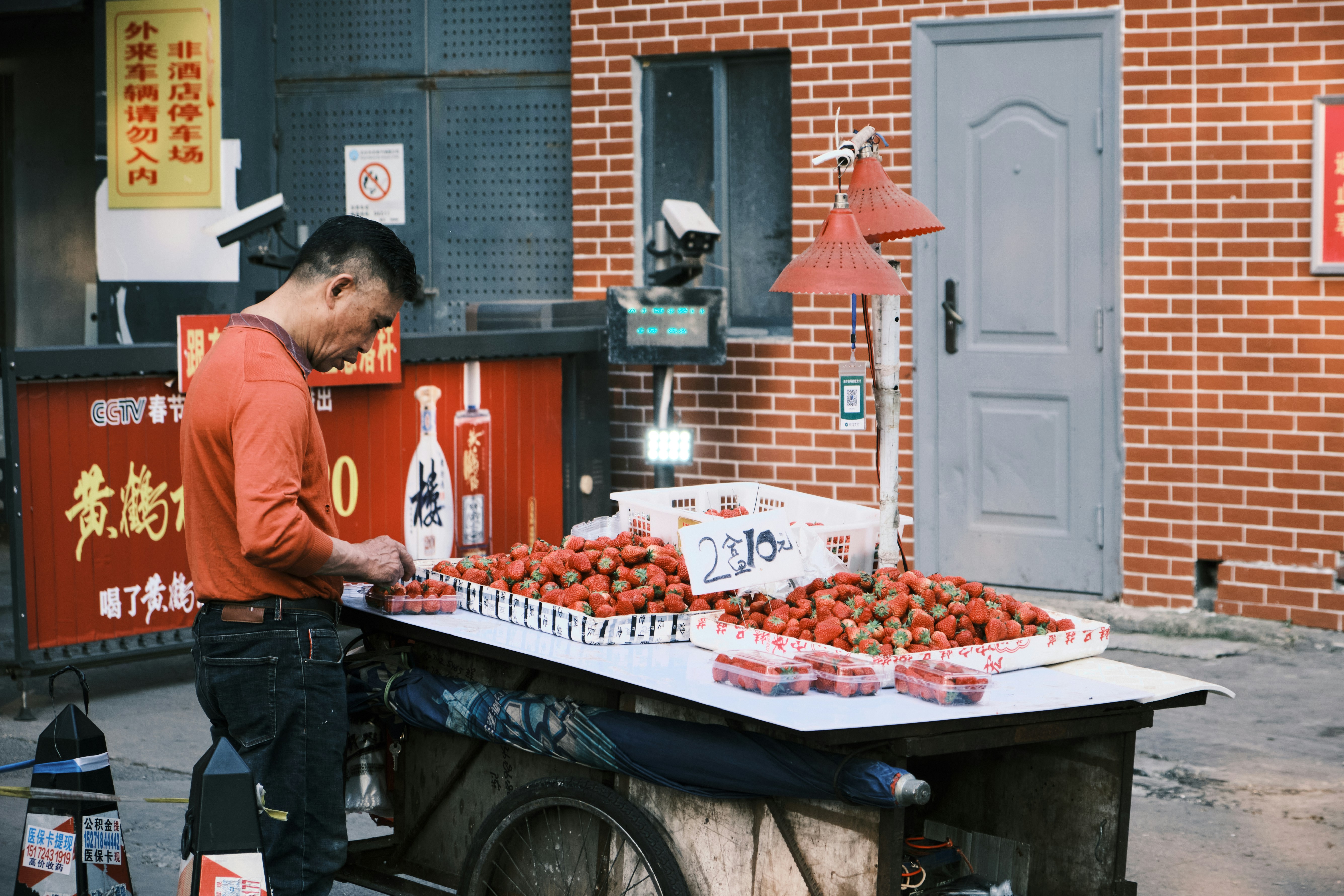 Street vendor arranging food on a cart in front of a brick wall and door.