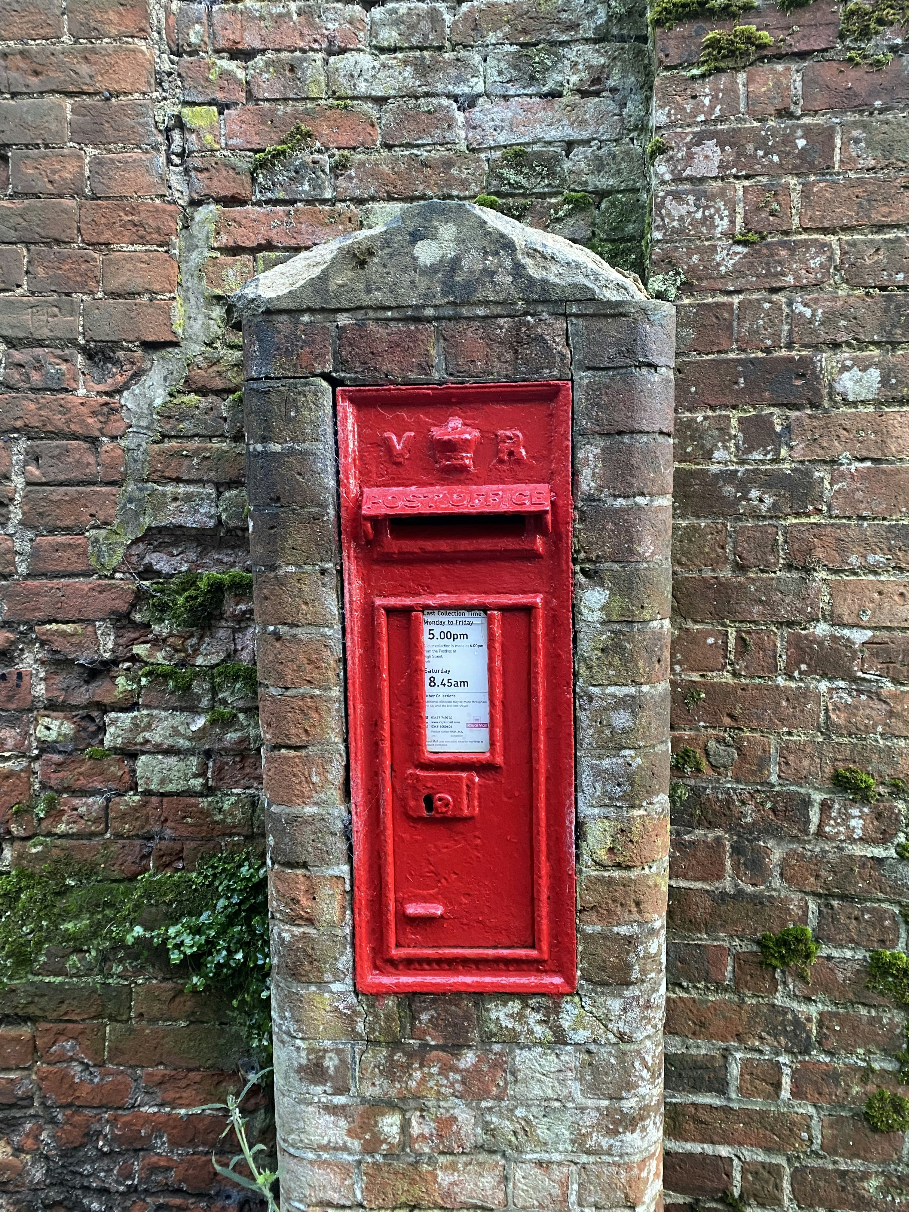 Scarlet Post Box Standing Guard on a Mossy Brick Wall
