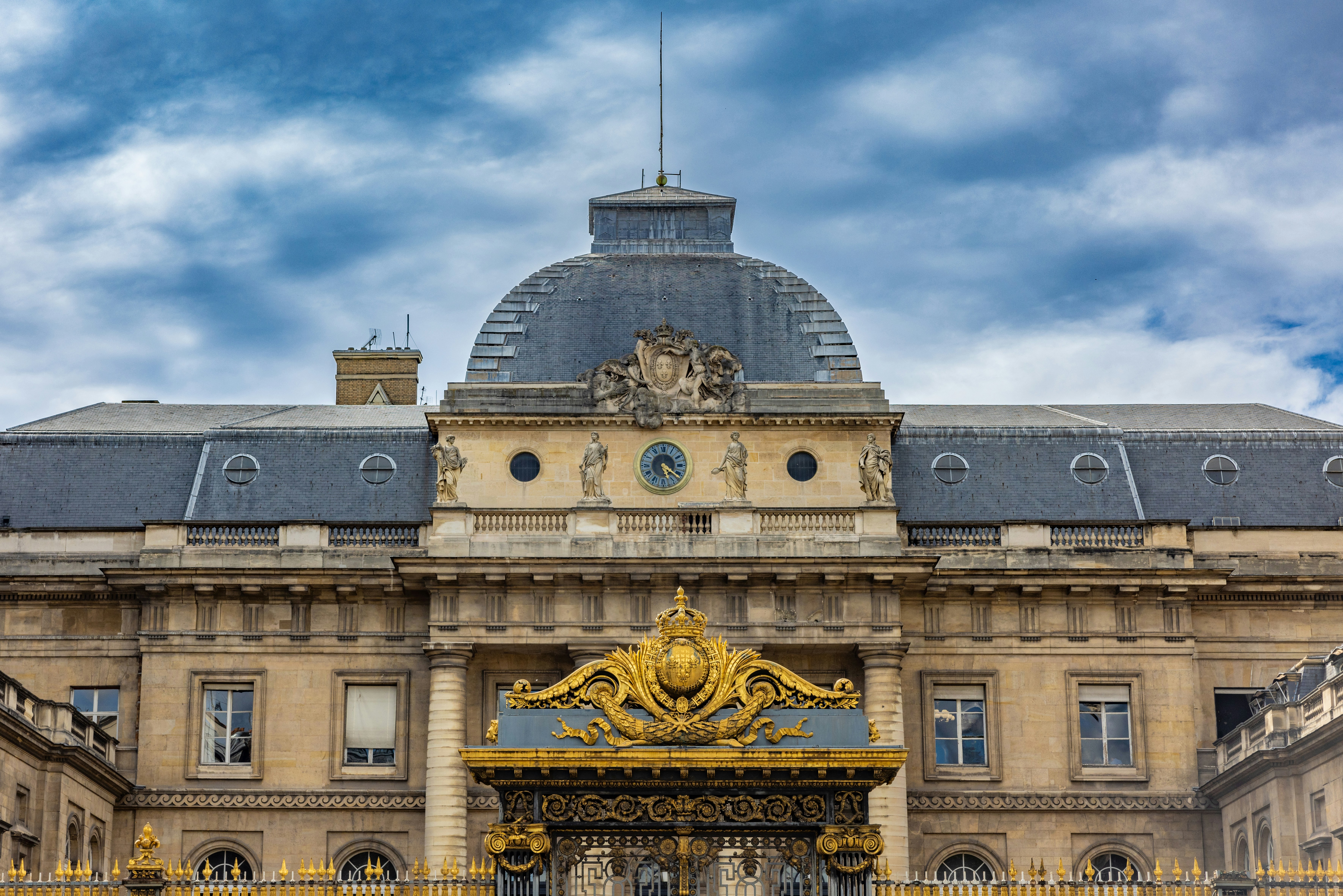 Elaborate architectural details of a historic building with a prominent golden gate and intricate rooftop design under a cloudy sky.