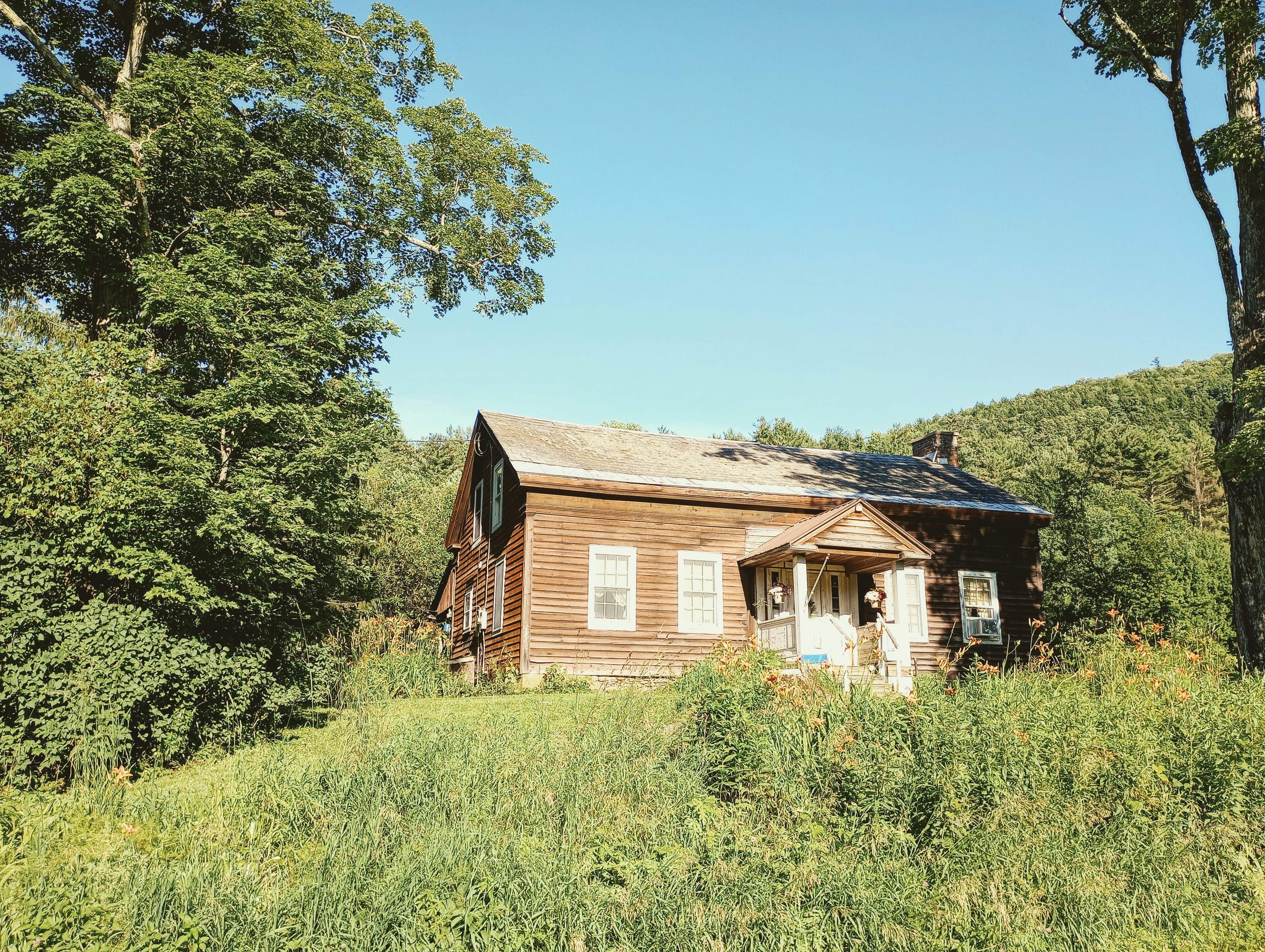 Historic farmhouse nestled among lush greenery under a clear blue sky.