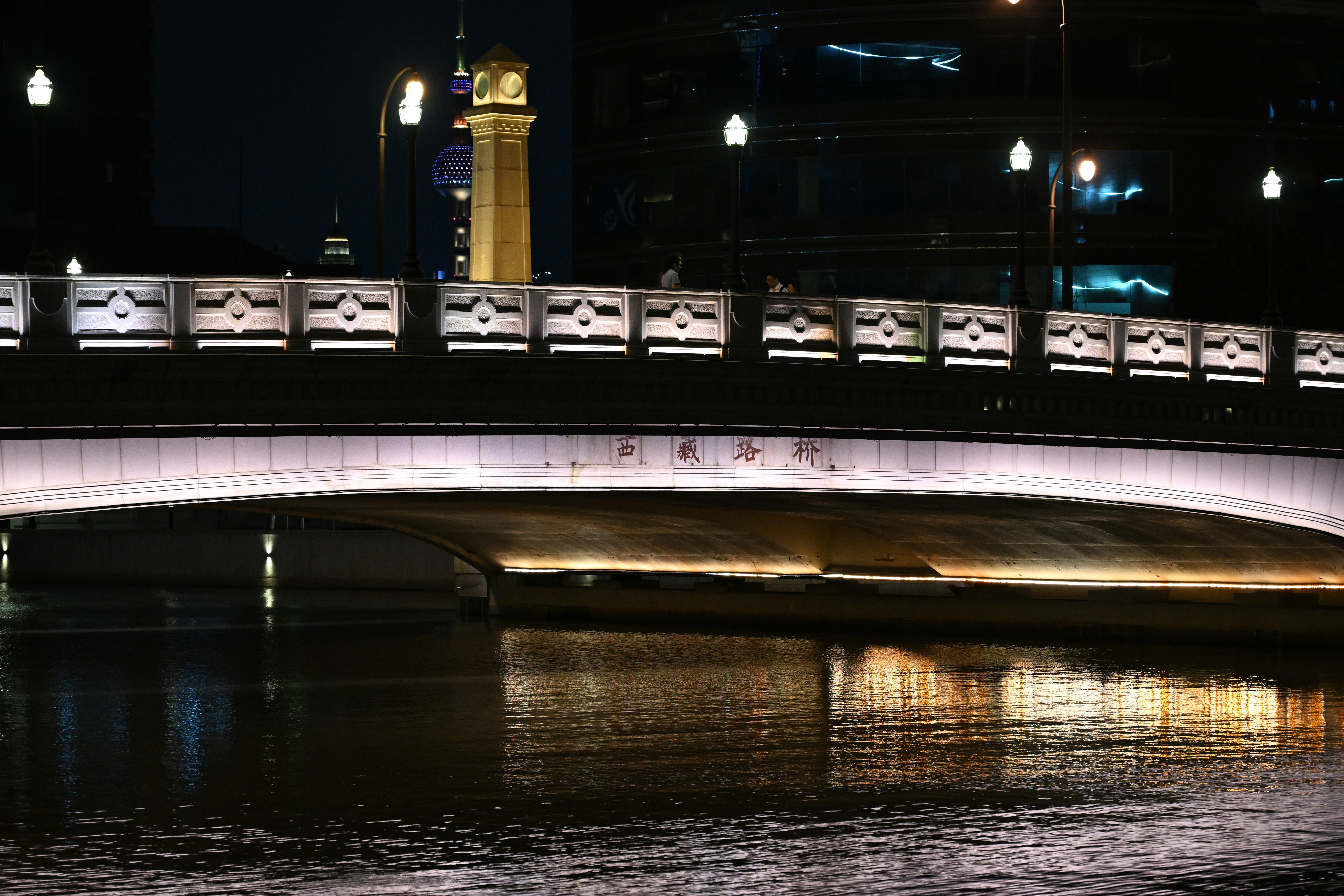 Luminous Clock Tower Over a Quiet River Bridge