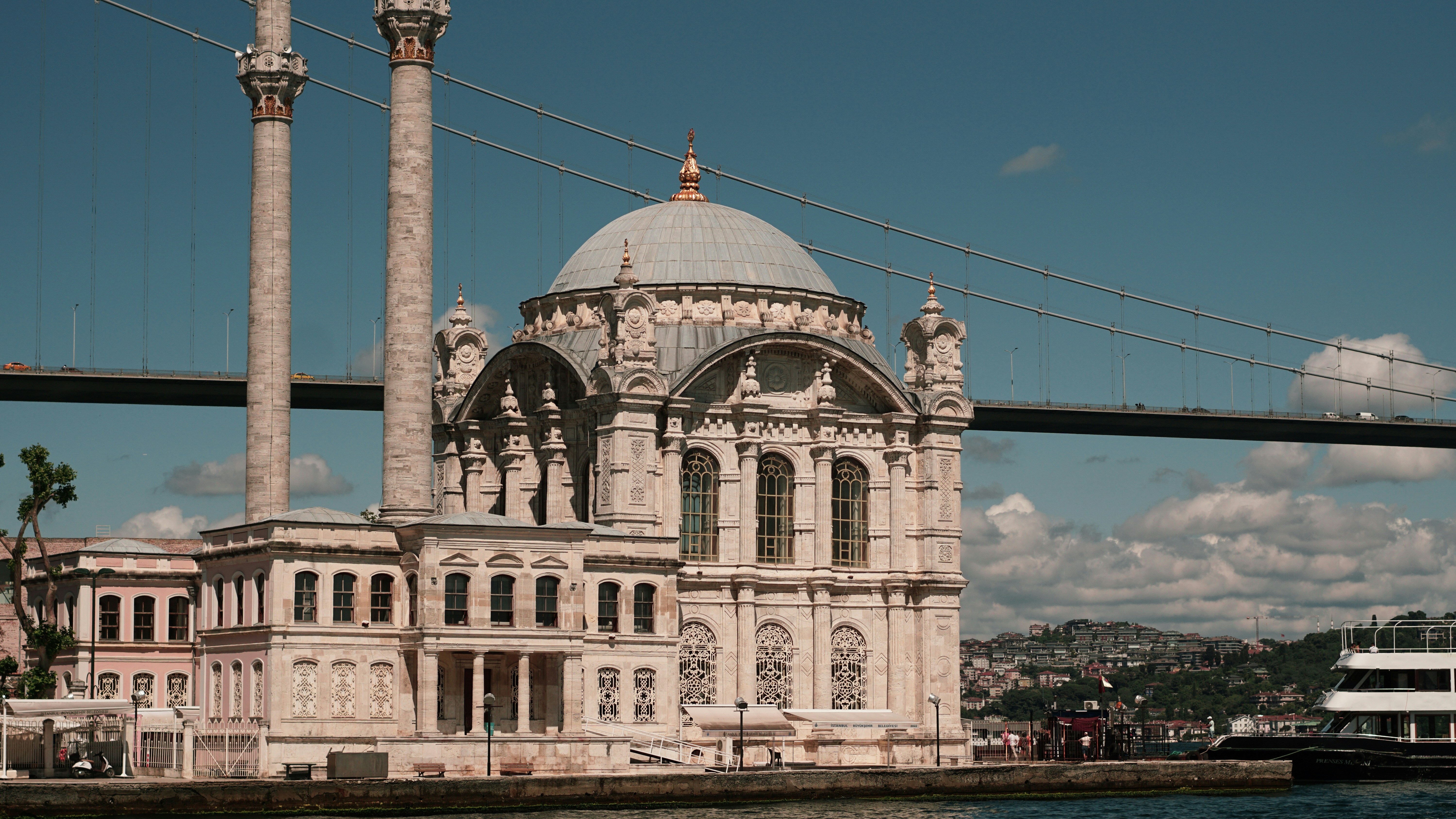 Ornate mosque with twin minarets beside a tranquil waterway under a clear blue sky.
