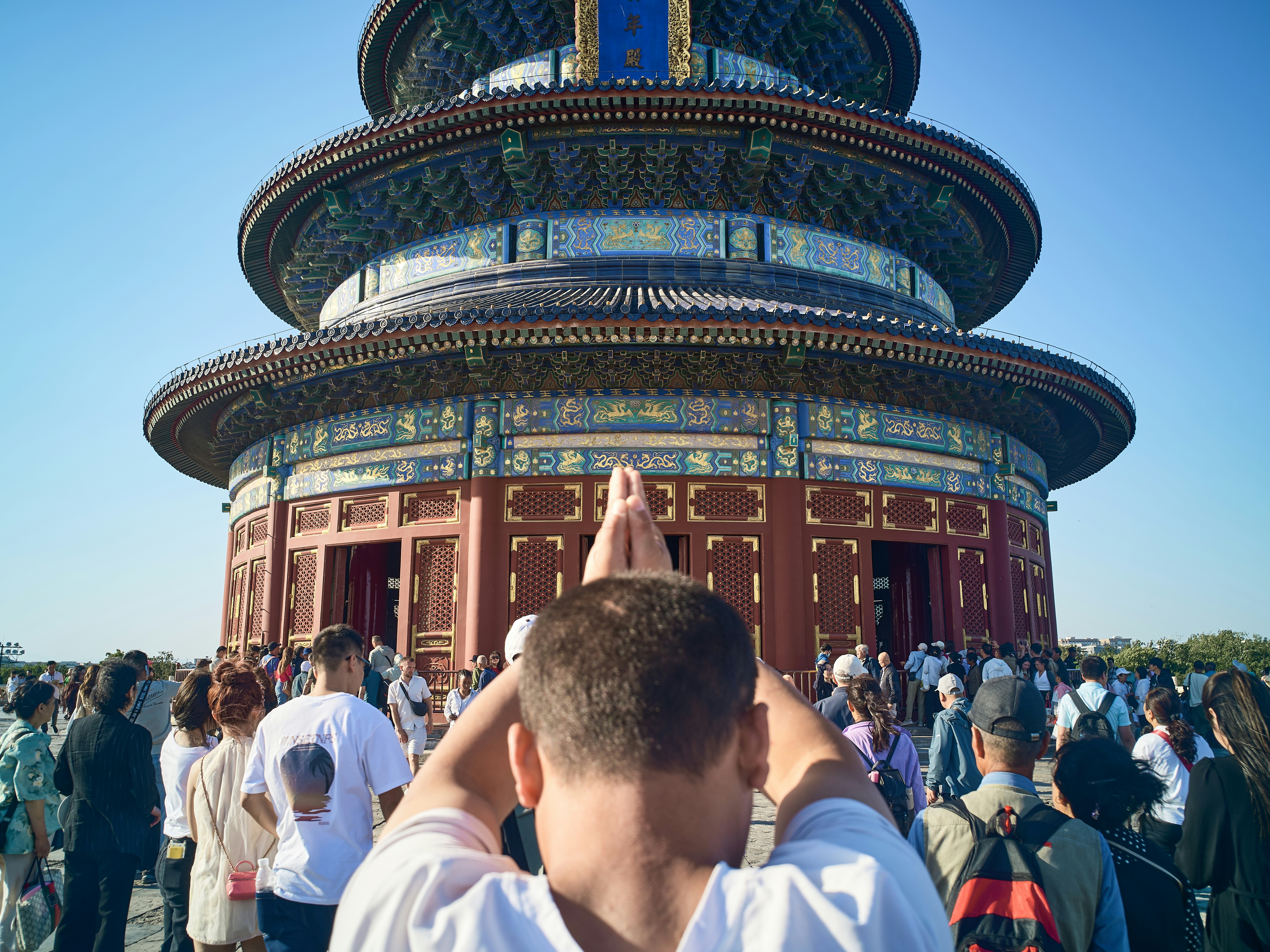 Crowd gathered around the ornate Temple of Heaven under a clear blue sky.