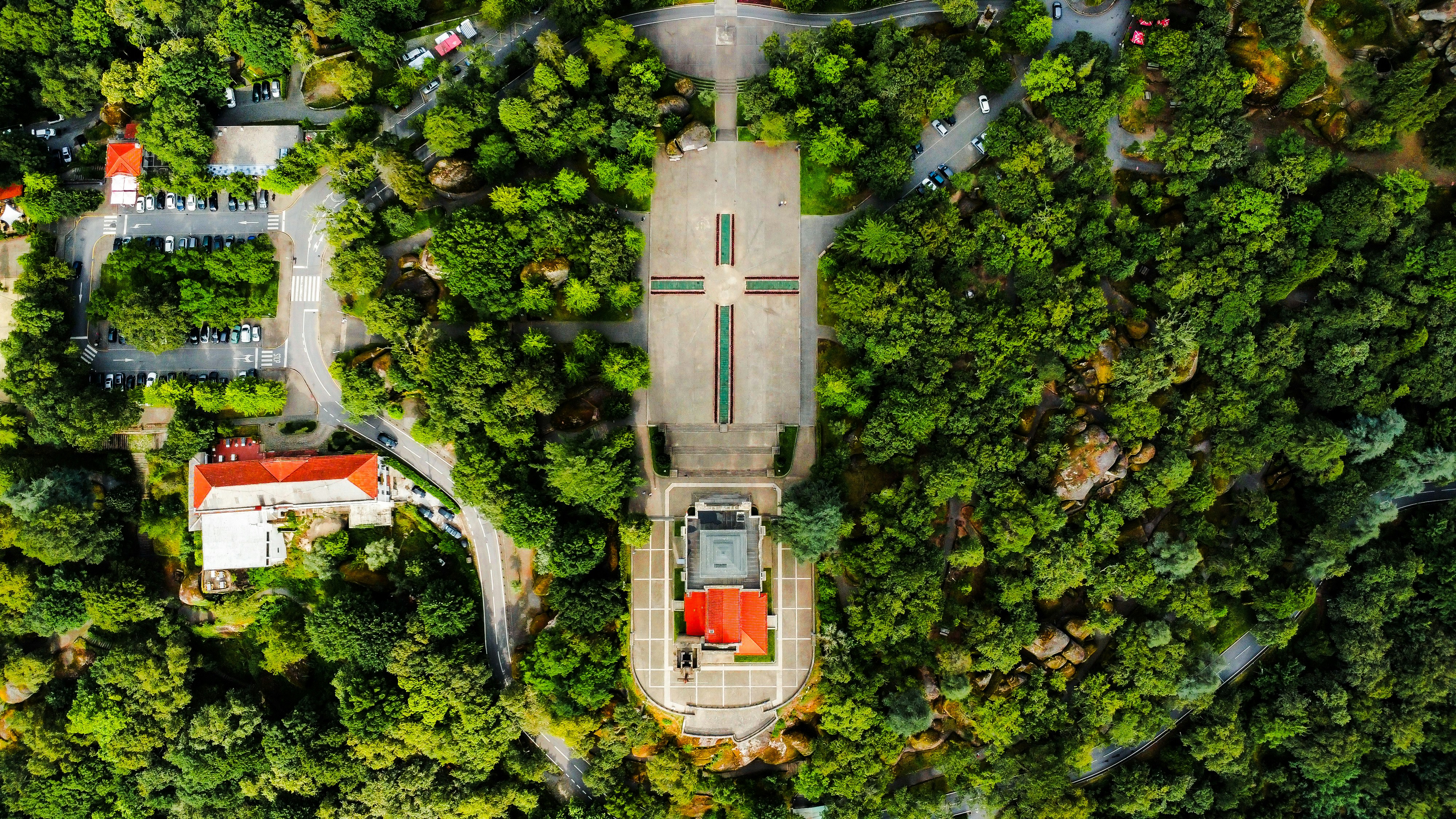Aerial photograph of a red-roofed pavilion nestled in a dense green forest, with pathways and surrounding structures forming a terraced complex.