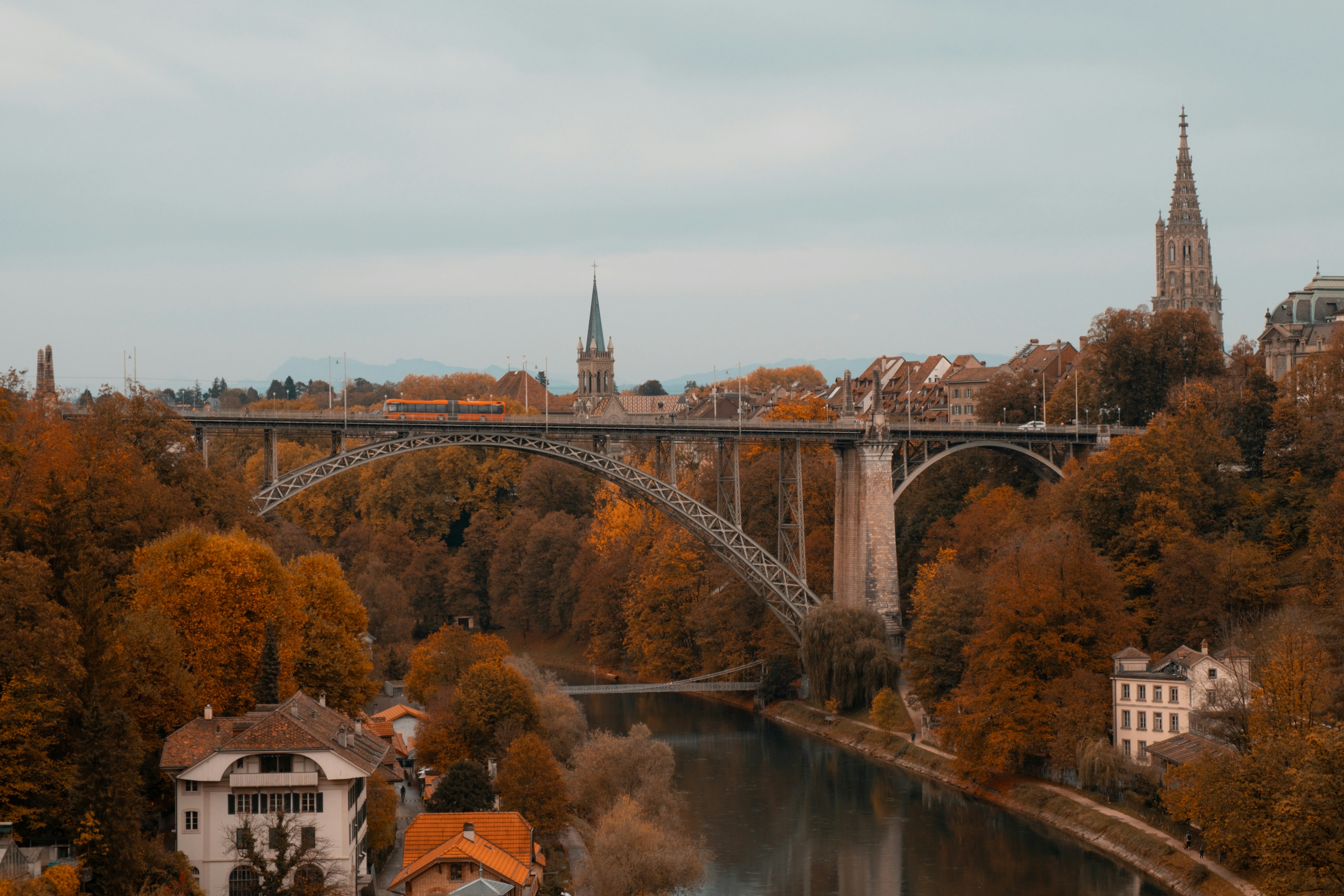 Historic bridge arches over a river surrounded by vibrant autumn foliage and classic European architecture.