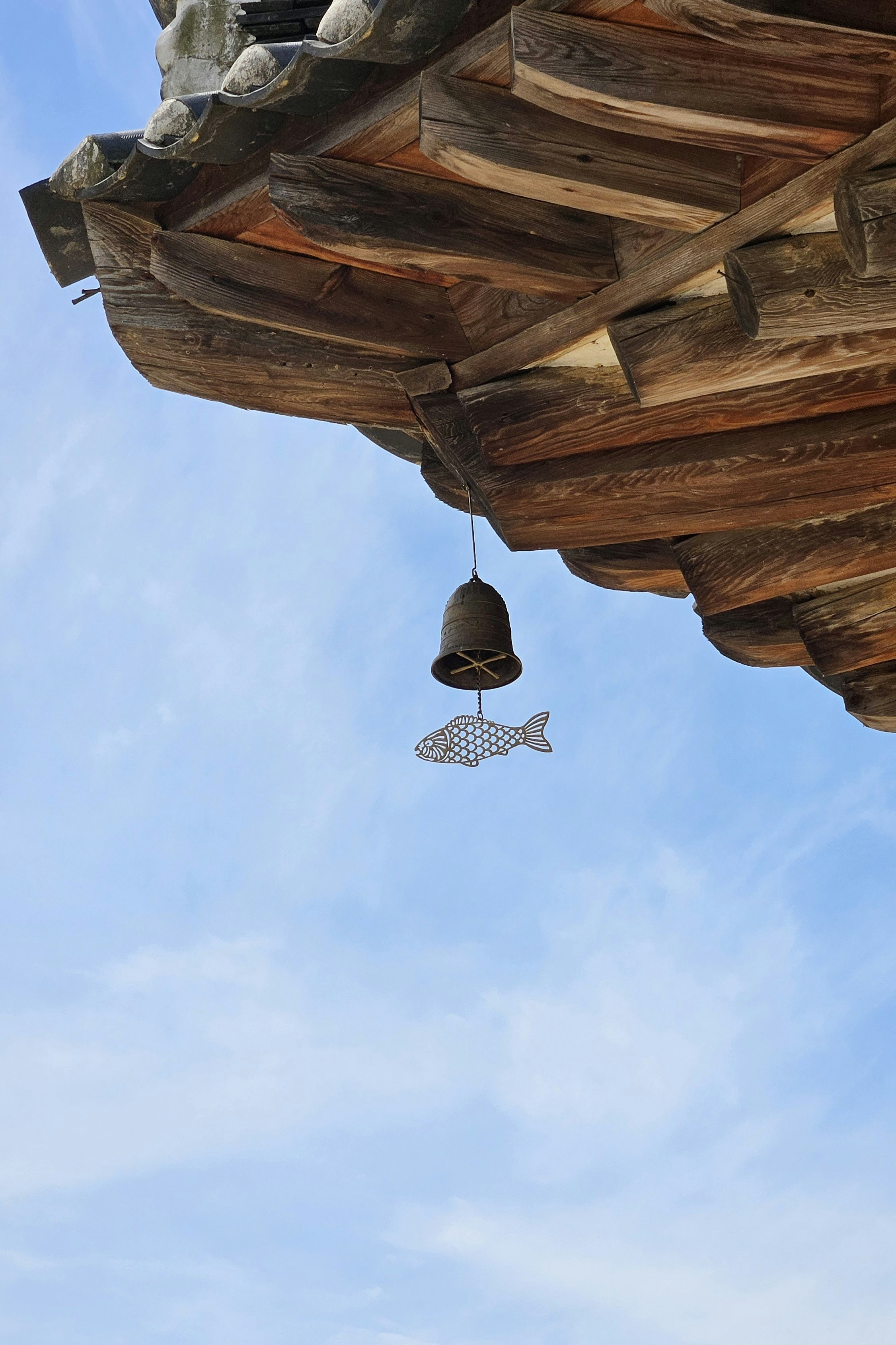 A bell hanging from the side of a wooden structure
