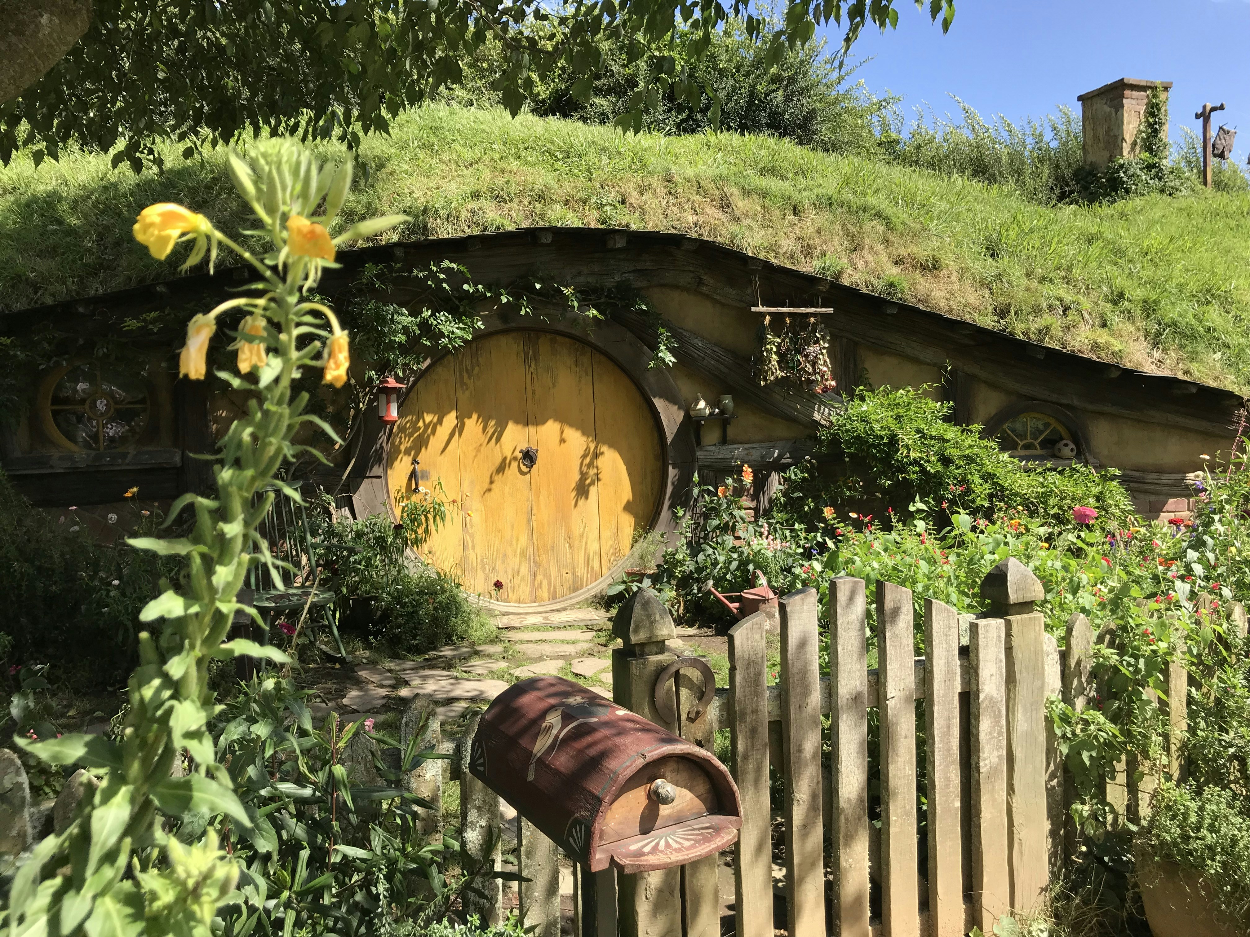 A hobbot house with a green roof and a wooden fence photo – Free Hobbit ...