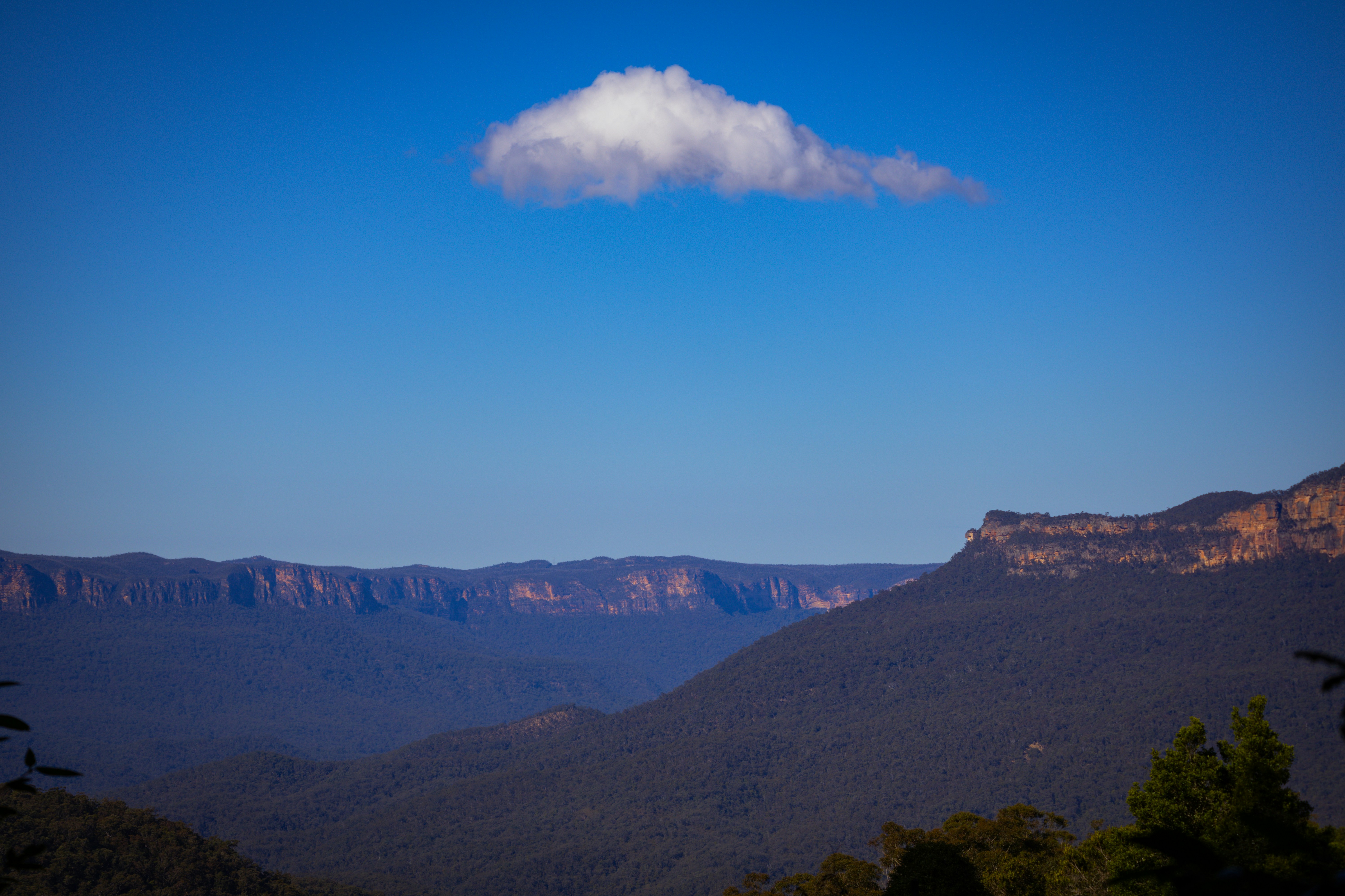 Lone Cloud Crowned Over Layered Canyon Ridges Under a Clear Sky