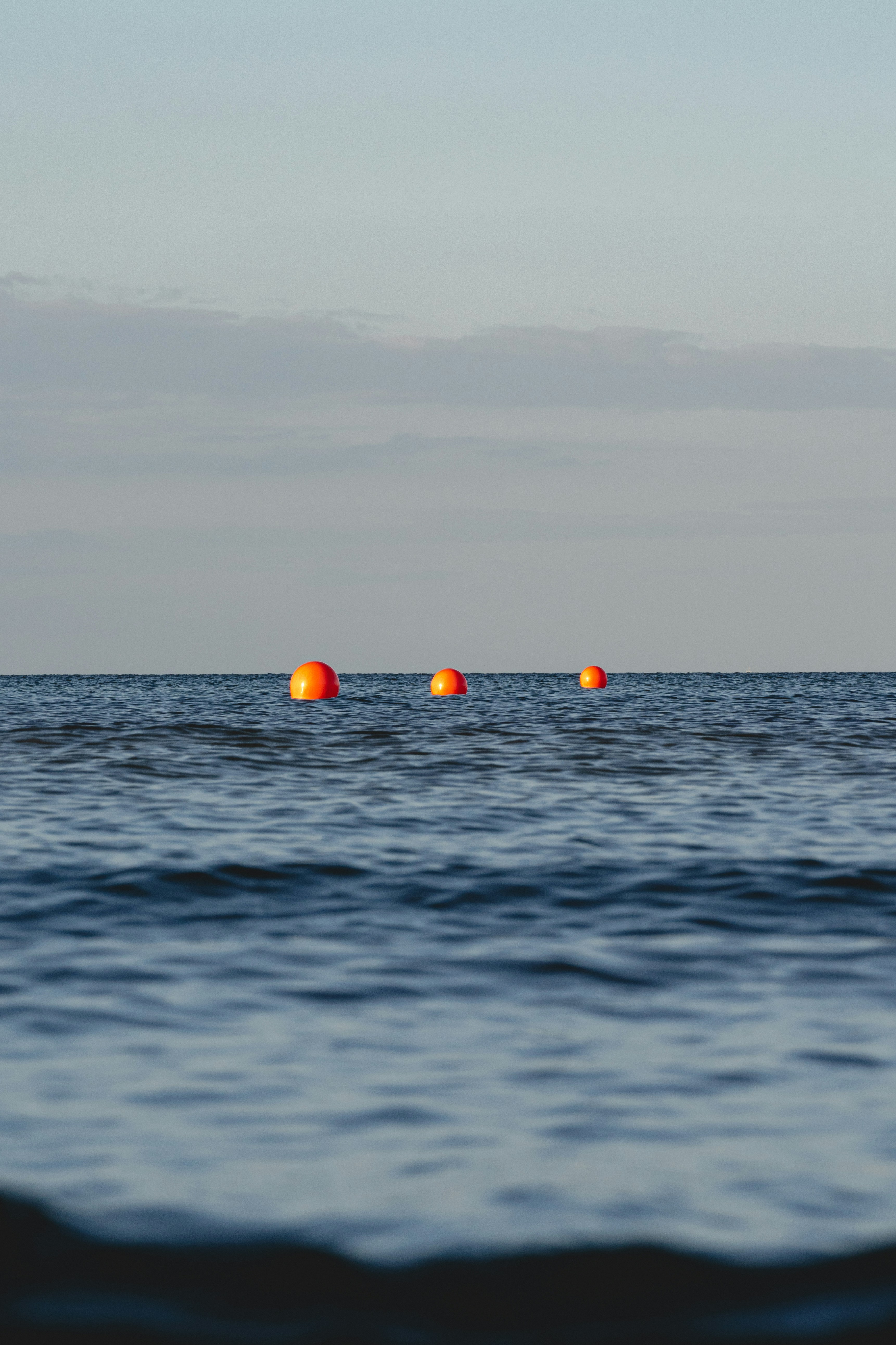 Three Orange Buoys Punctuate a Calm Ocean Horizon