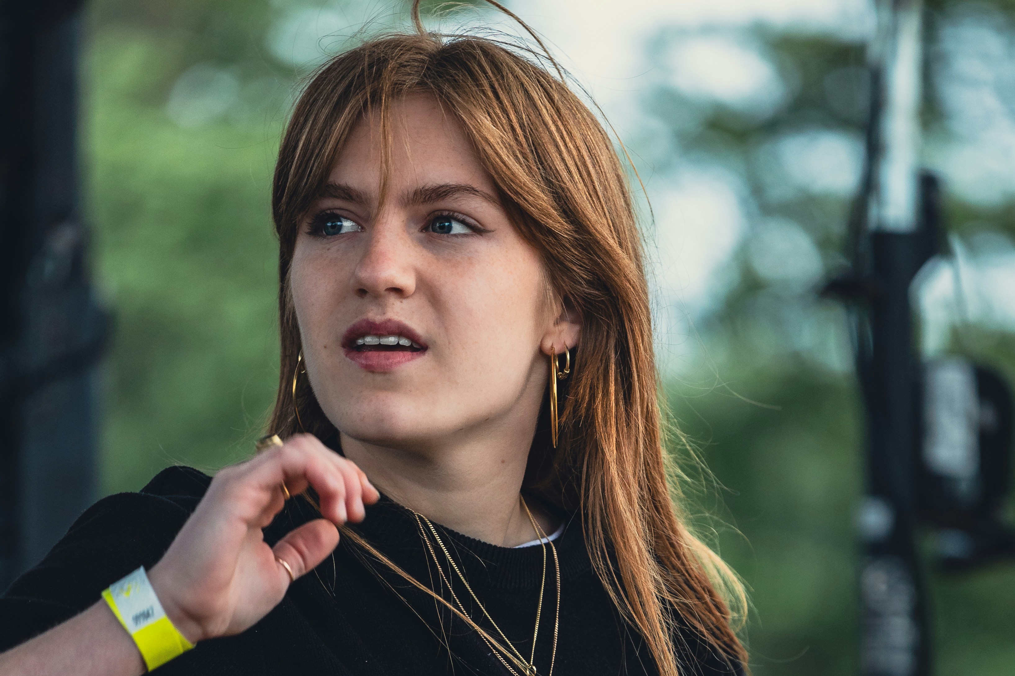 Young woman with auburn hair and gold jewelry gazing to the side outdoors.