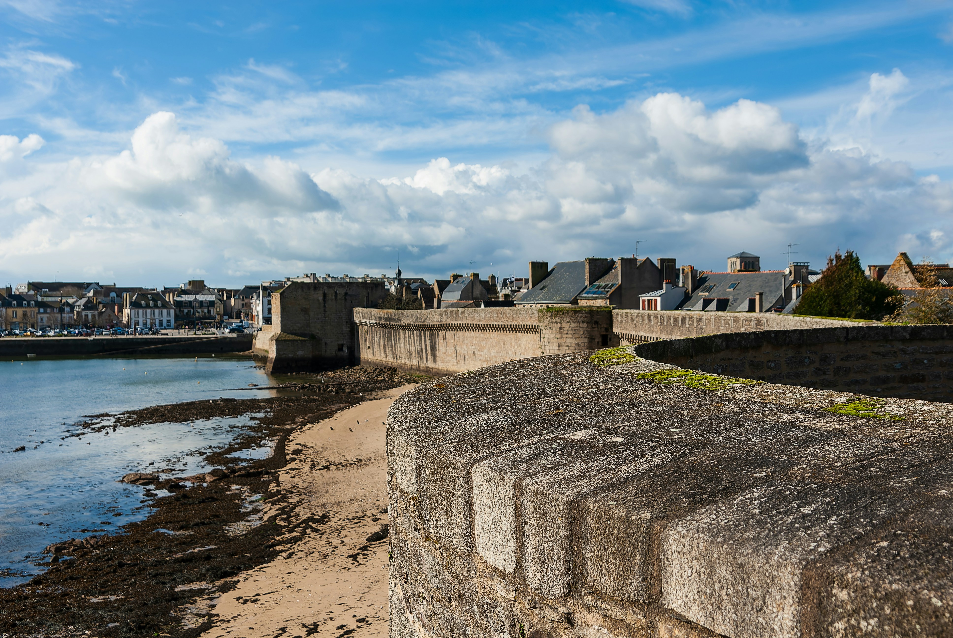 Stone ramparts overlooking a coastal town with scattered clouds in a bright blue sky.