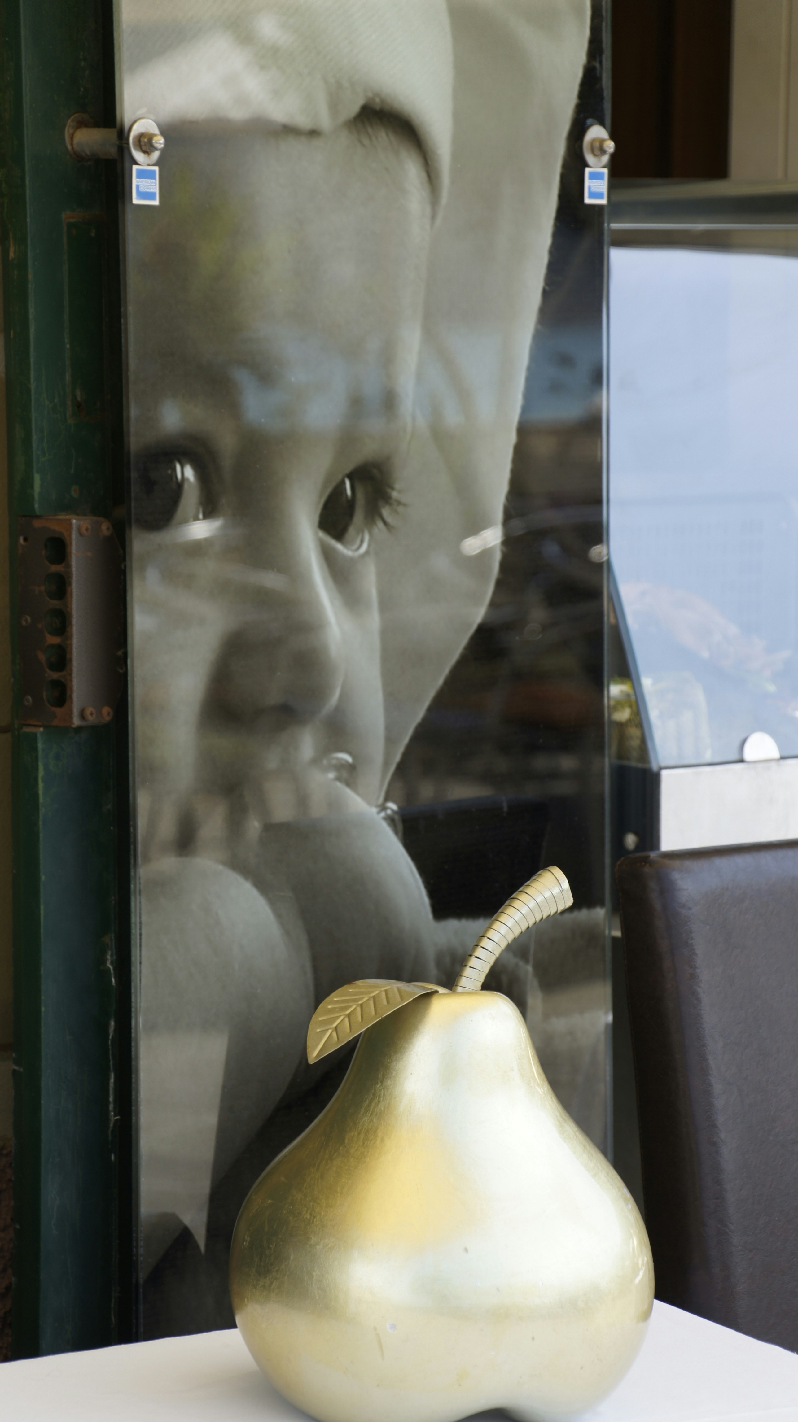 Glass-Front Gaze: A Doll’s Face Reflected Behind a Golden Pear