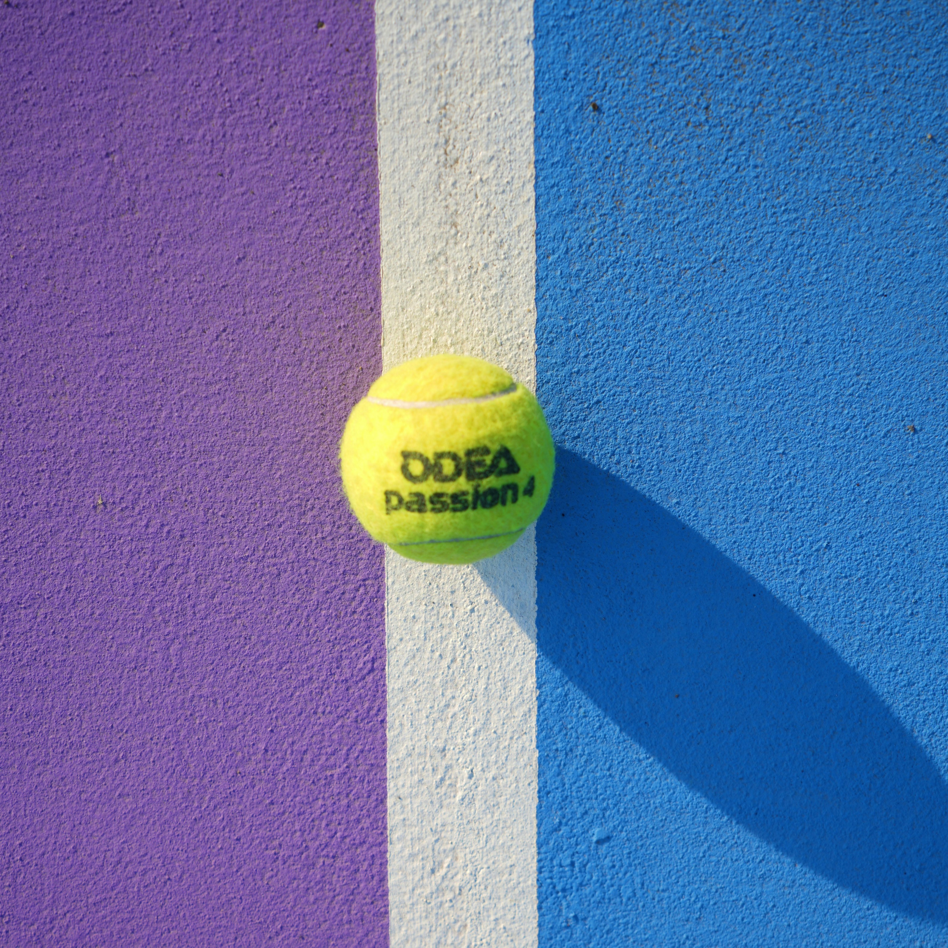 Una pelota de tenis amarilla colocada sobre una pared morada y blanca ...