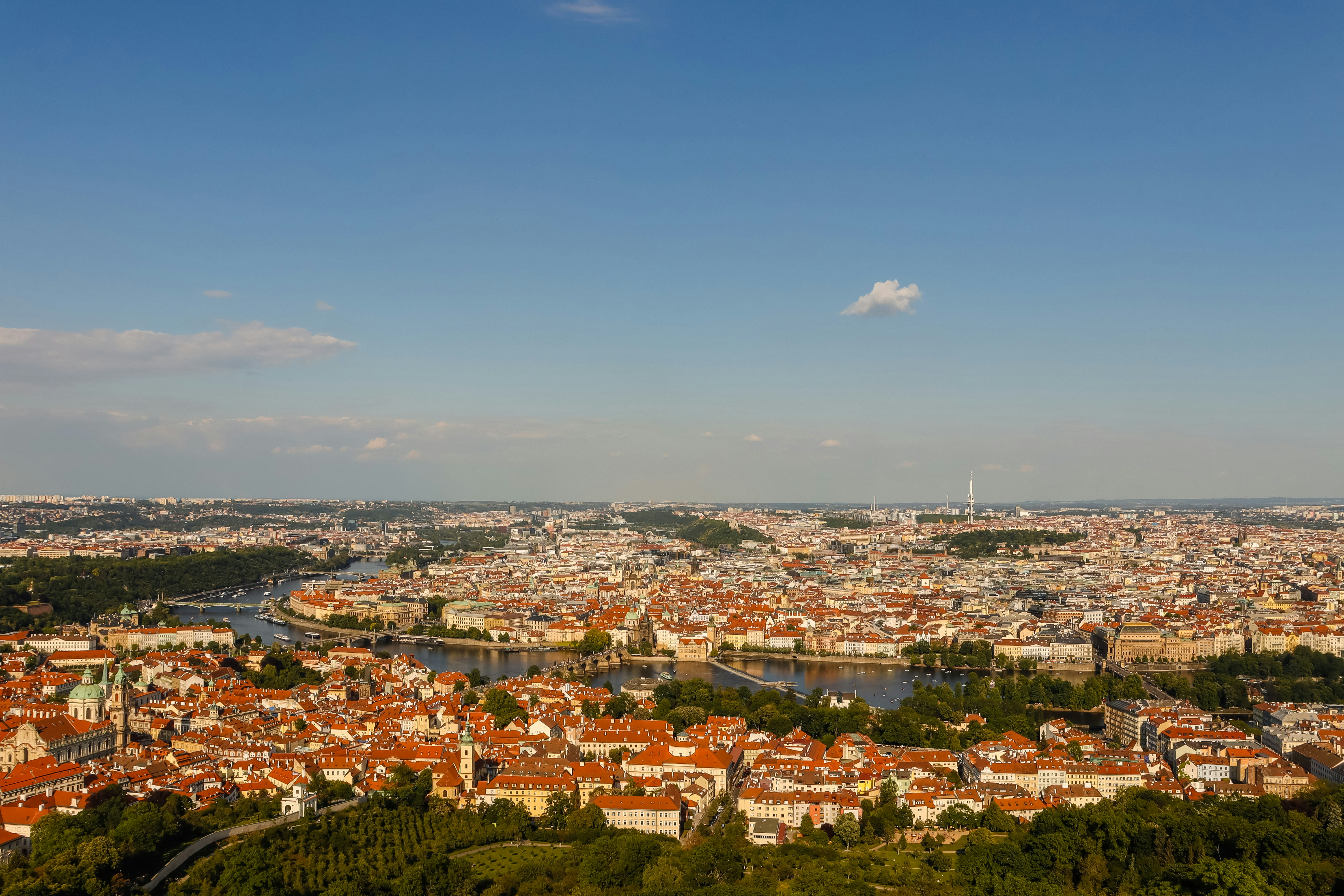 Panoramic view of Prague's historic red rooftops and the winding Vltava River under a clear blue sky.