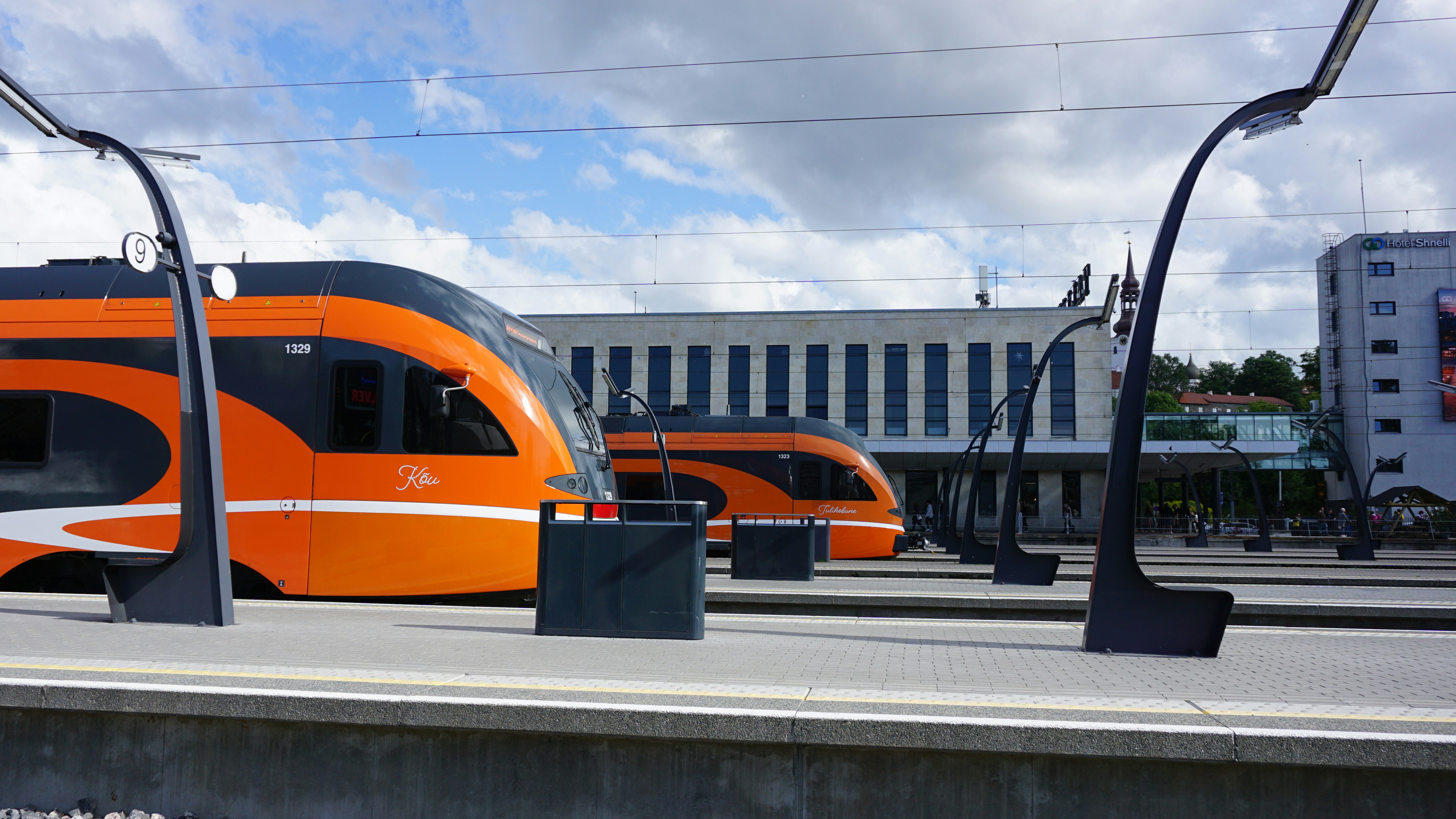 Bright orange trains parked at a modern station under a partly cloudy sky.