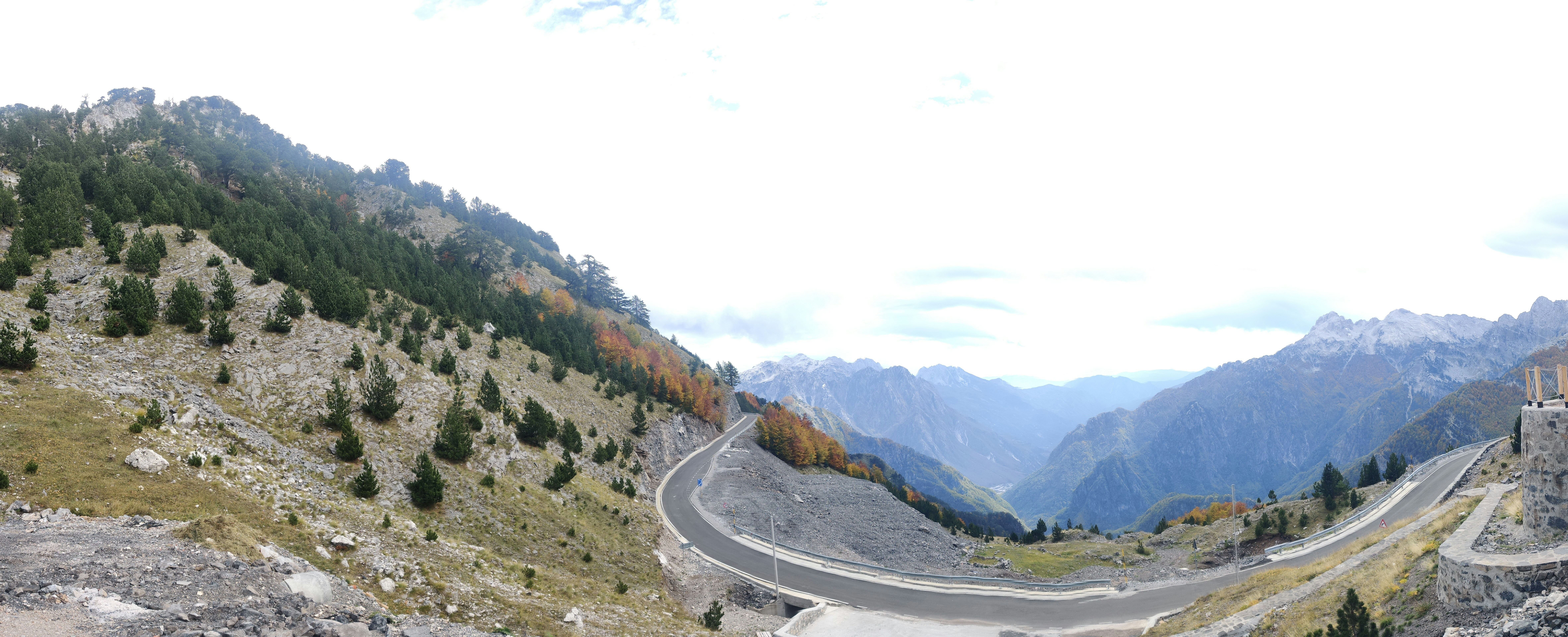 Curving mountain road surrounded by rocky hills and distant blue peaks under a cloudy sky.