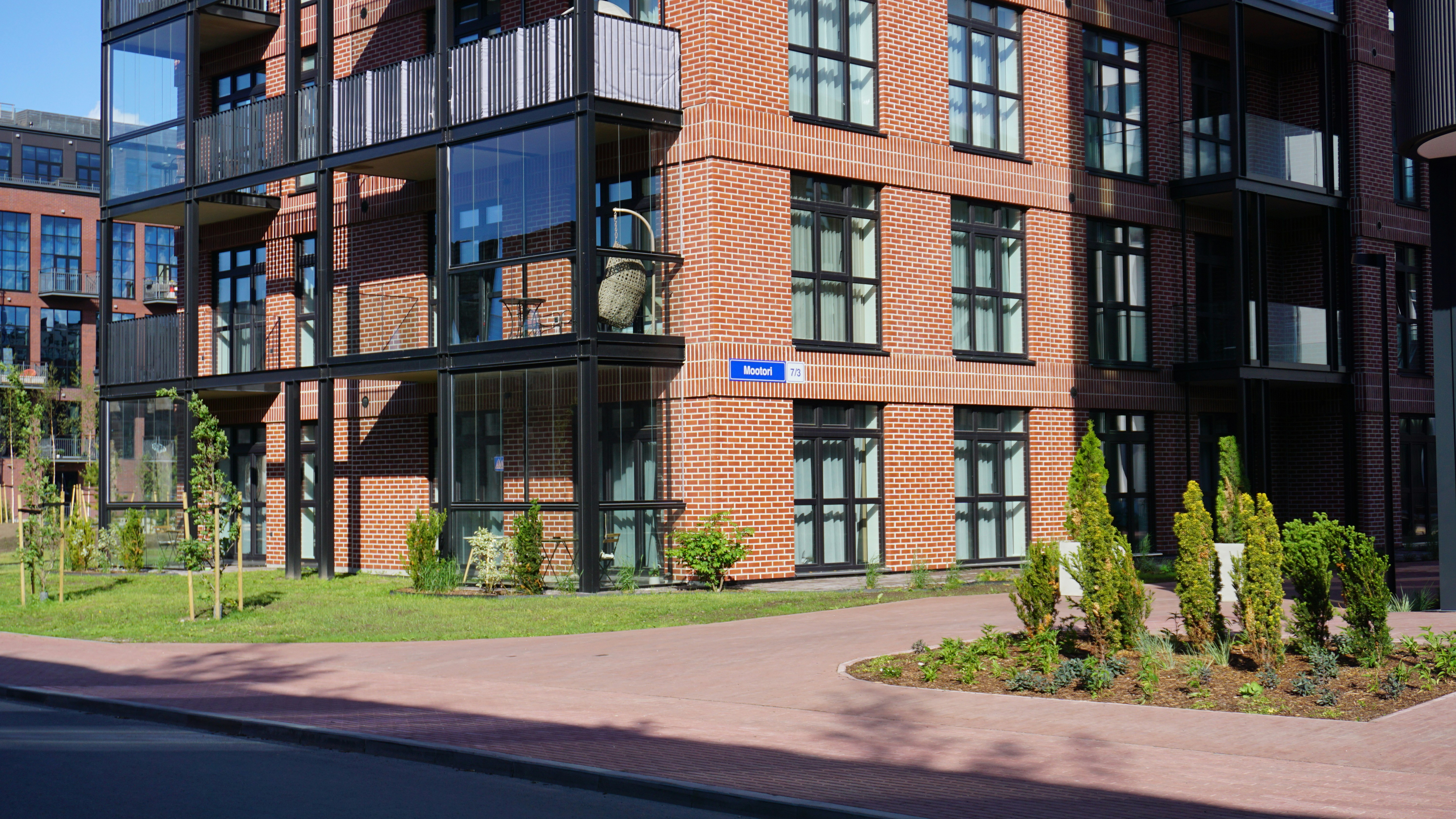 Contemporary brick apartment building with large glass balconies and landscaped greenery under clear blue skies.
