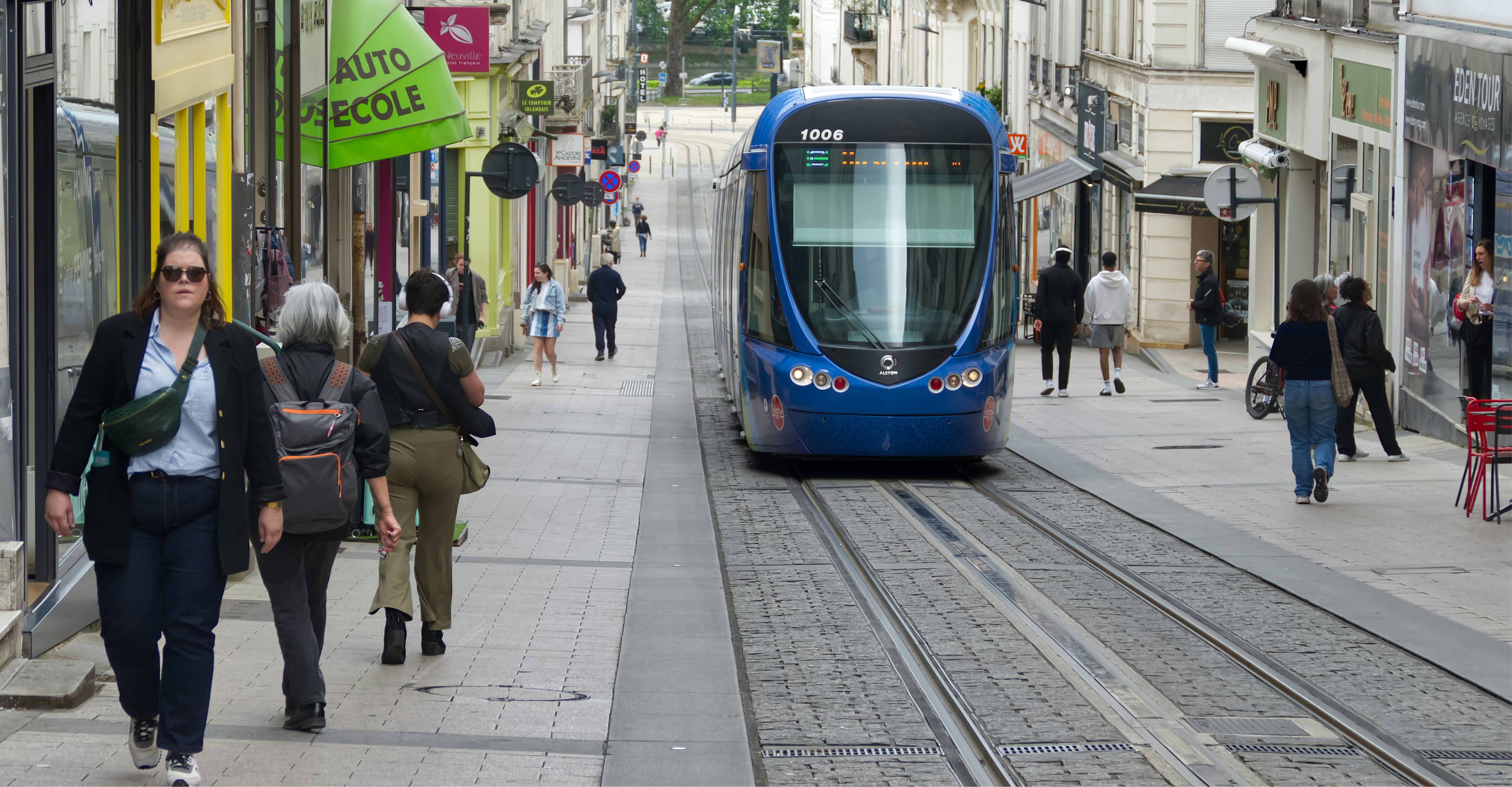 Blue tram traveling down a bustling street in Angers, surrounded by pedestrians and shops.