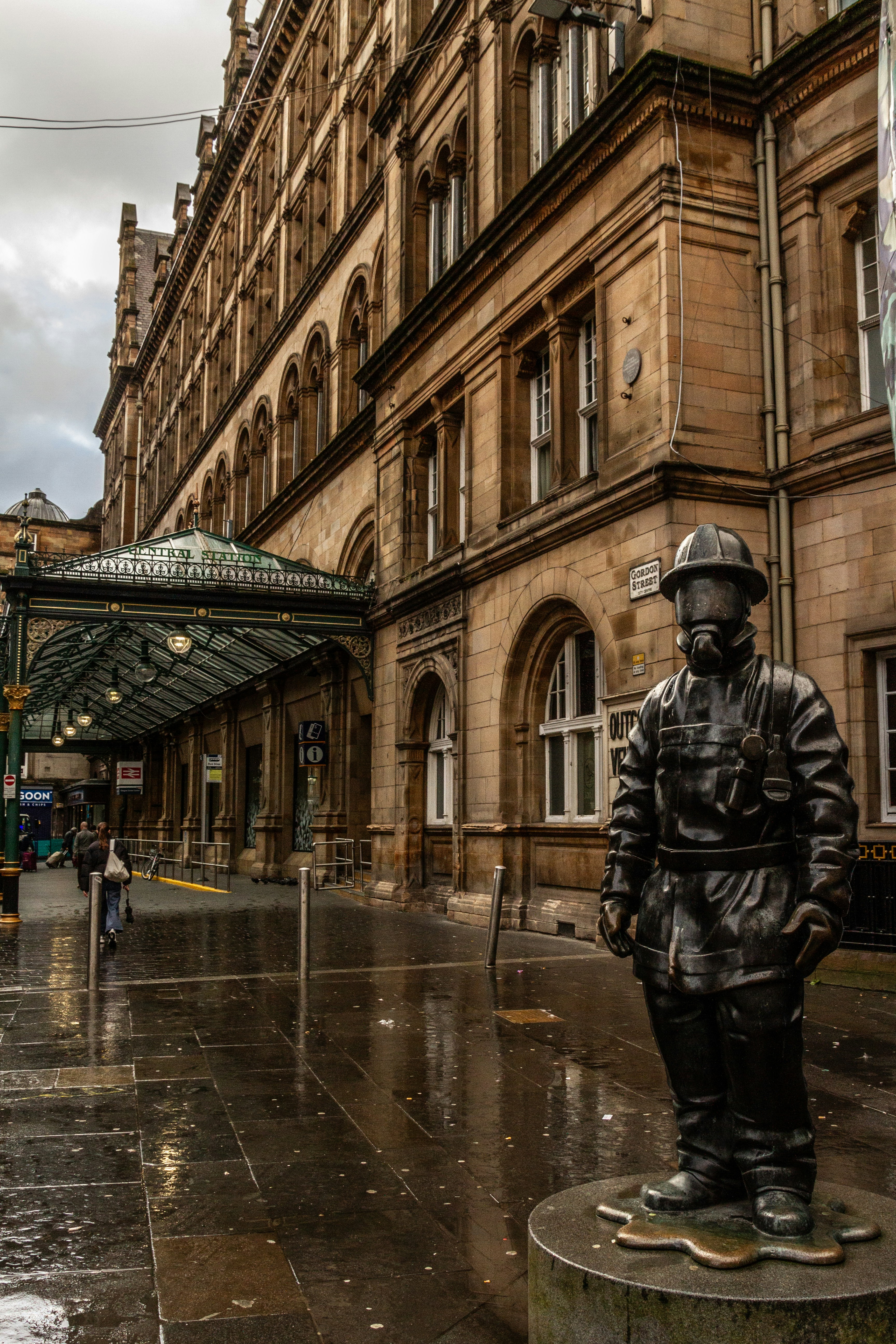 Bronze Firefighter Guardian at a Rain-Washed City Station Façade