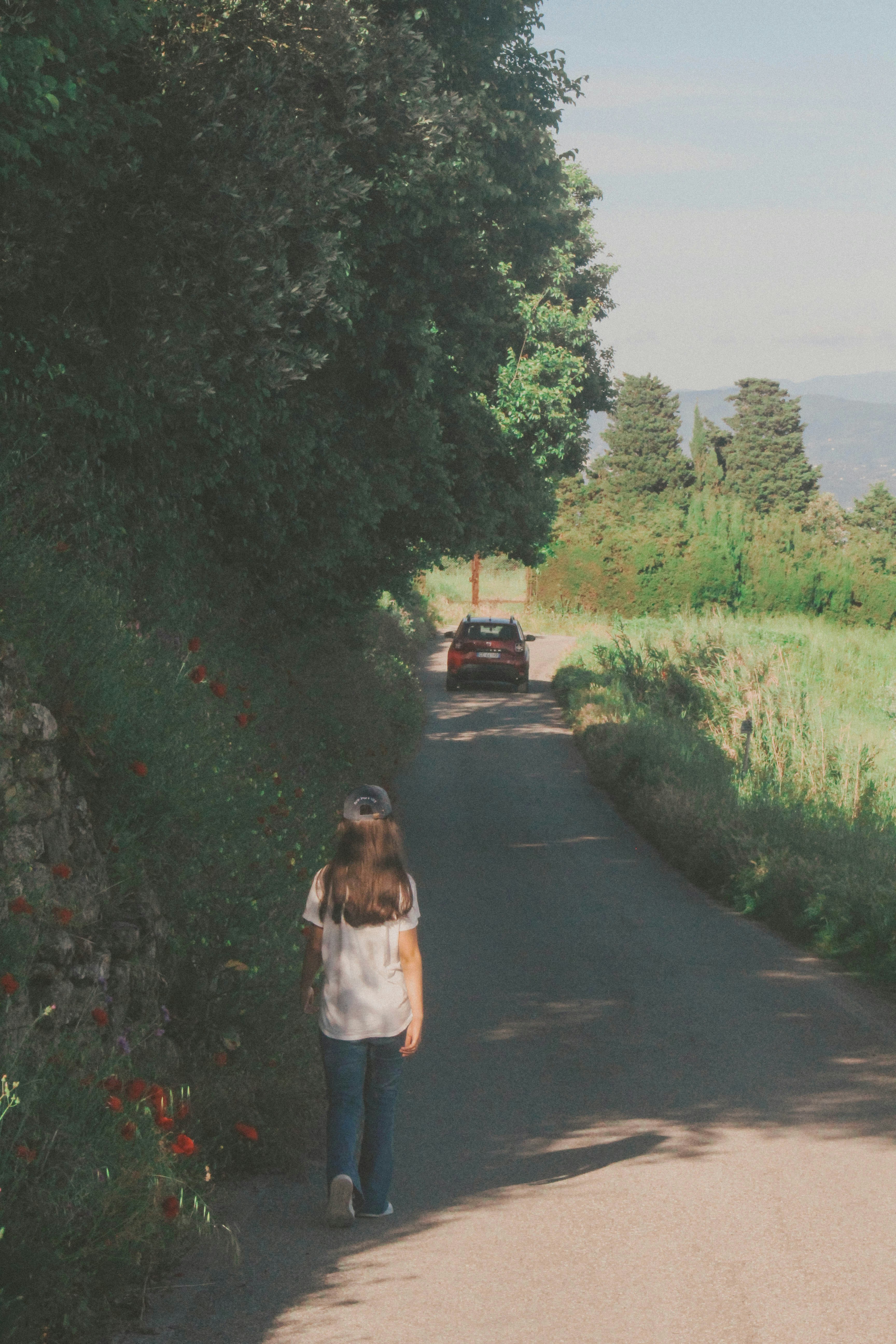 Sunlit Quiet: A Girl Walks Toward a Distant Car on a Narrow Country Path