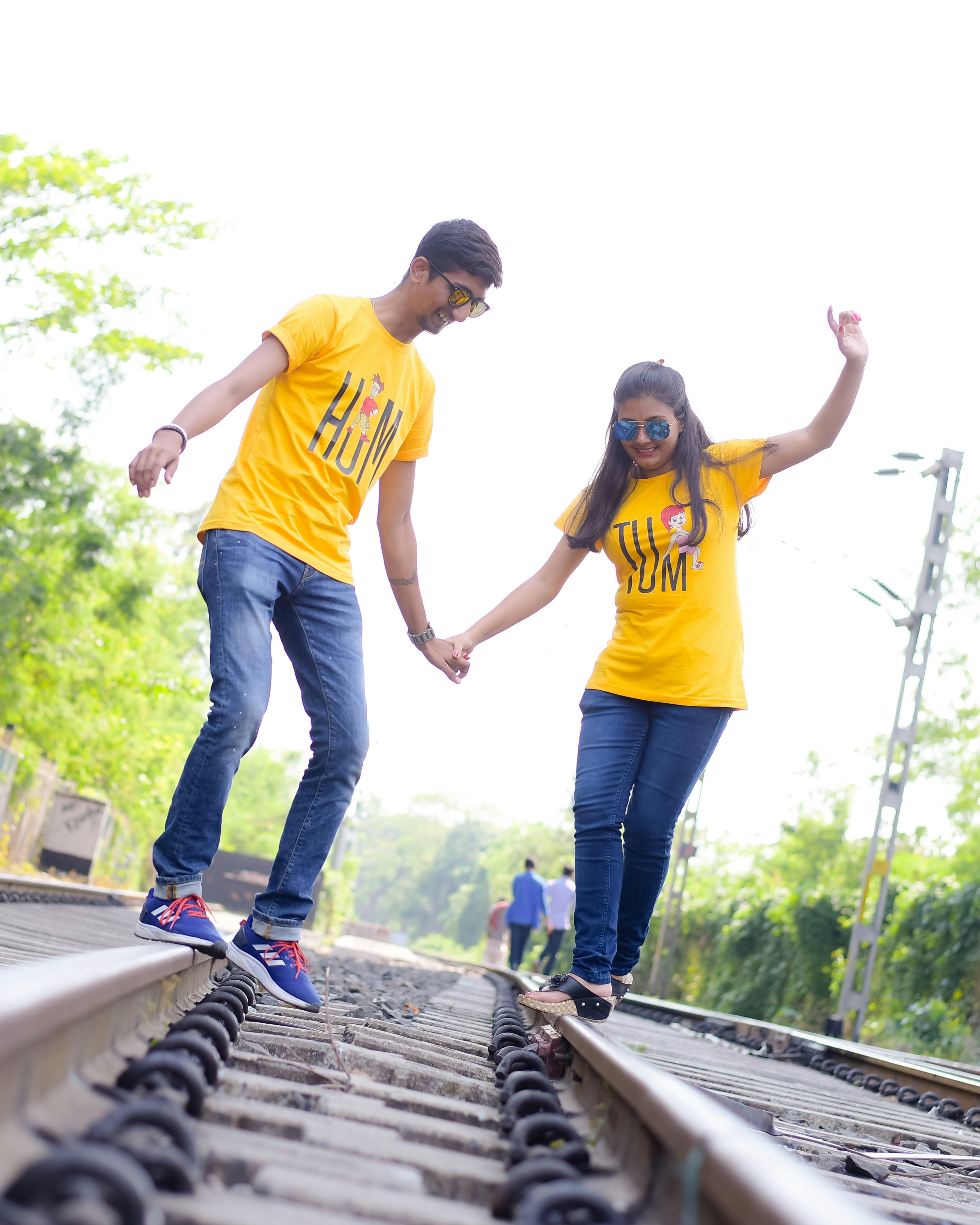 Sunlit Balance: A duo in matching yellow tees walk the rails hand in hand