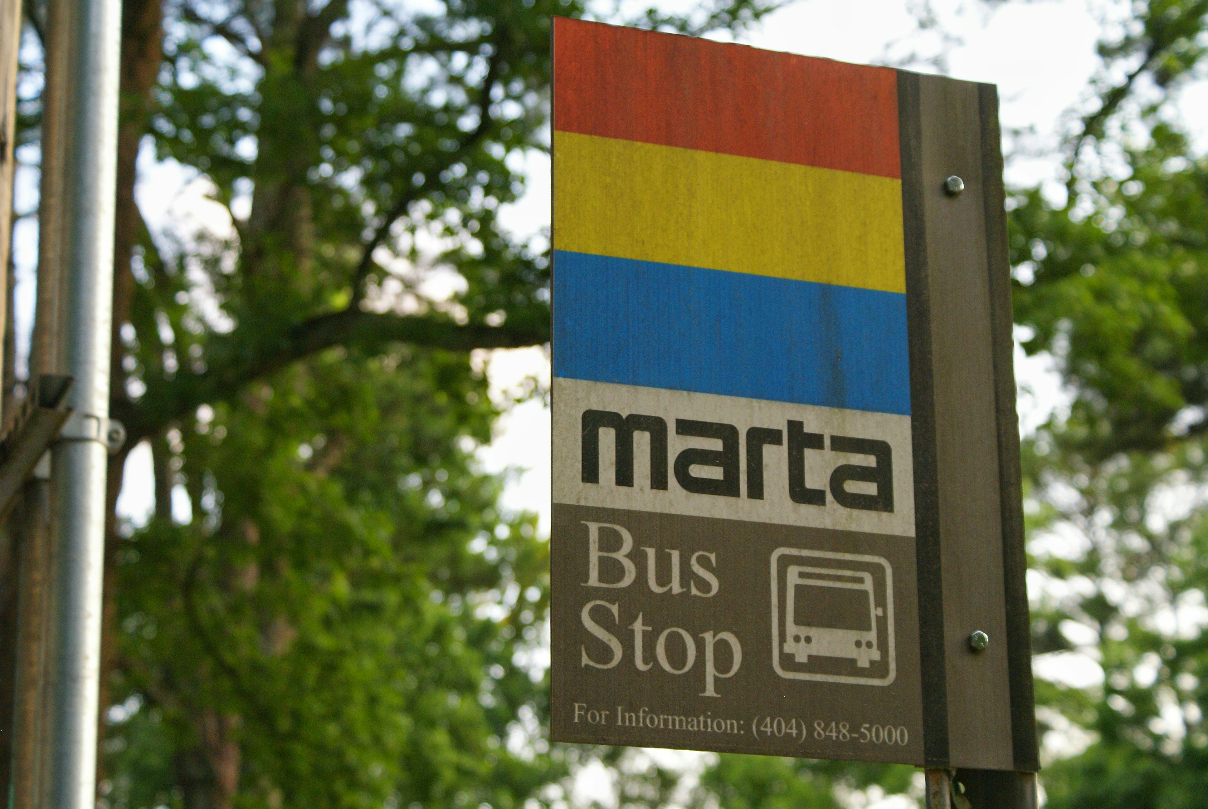 Tri-Color Marta Bus Stop Sign Against a Verdant Urban Canopy