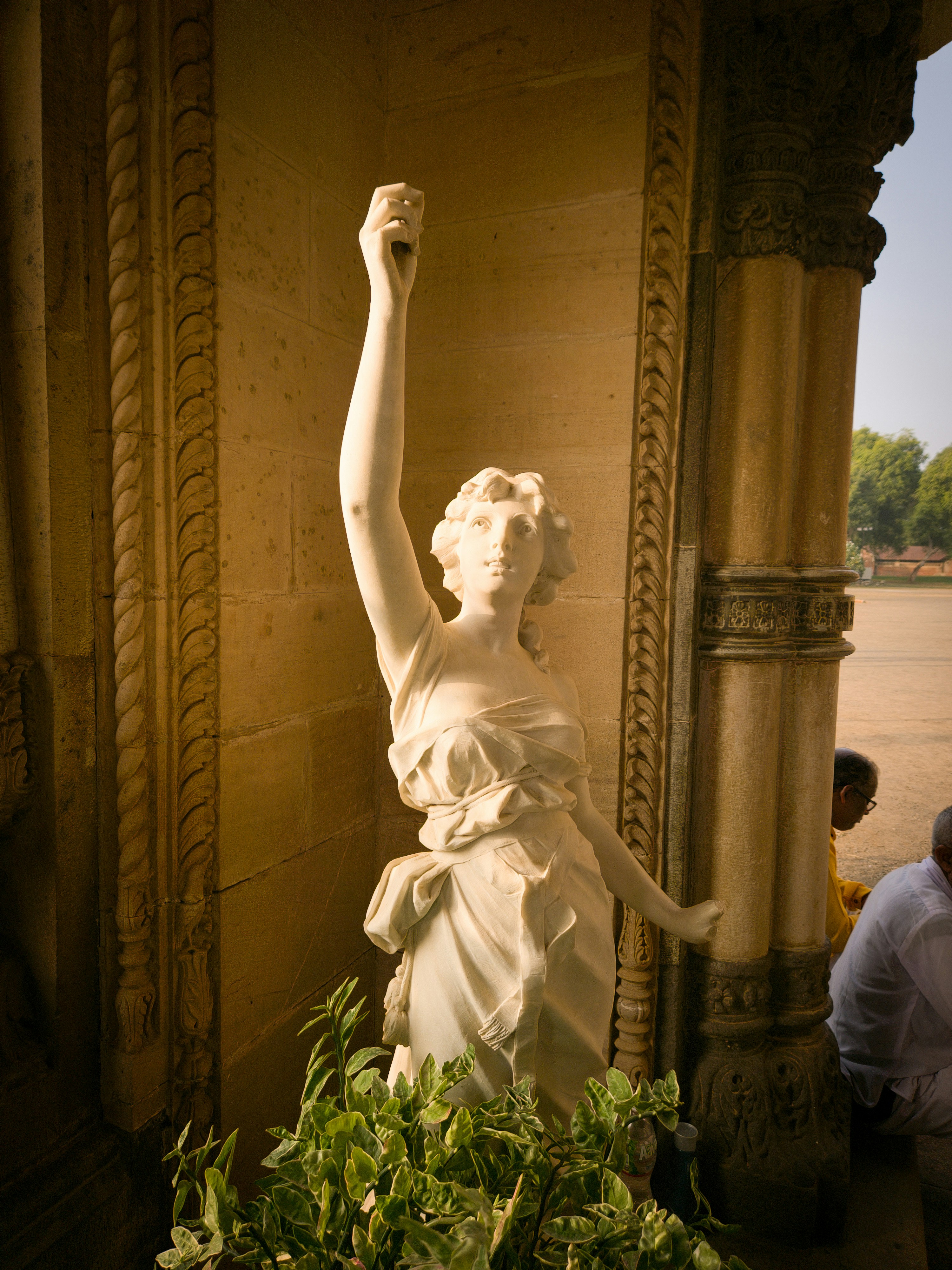 Statue in Stone Arcade: Sunlit Pose Amid Ancient Columns