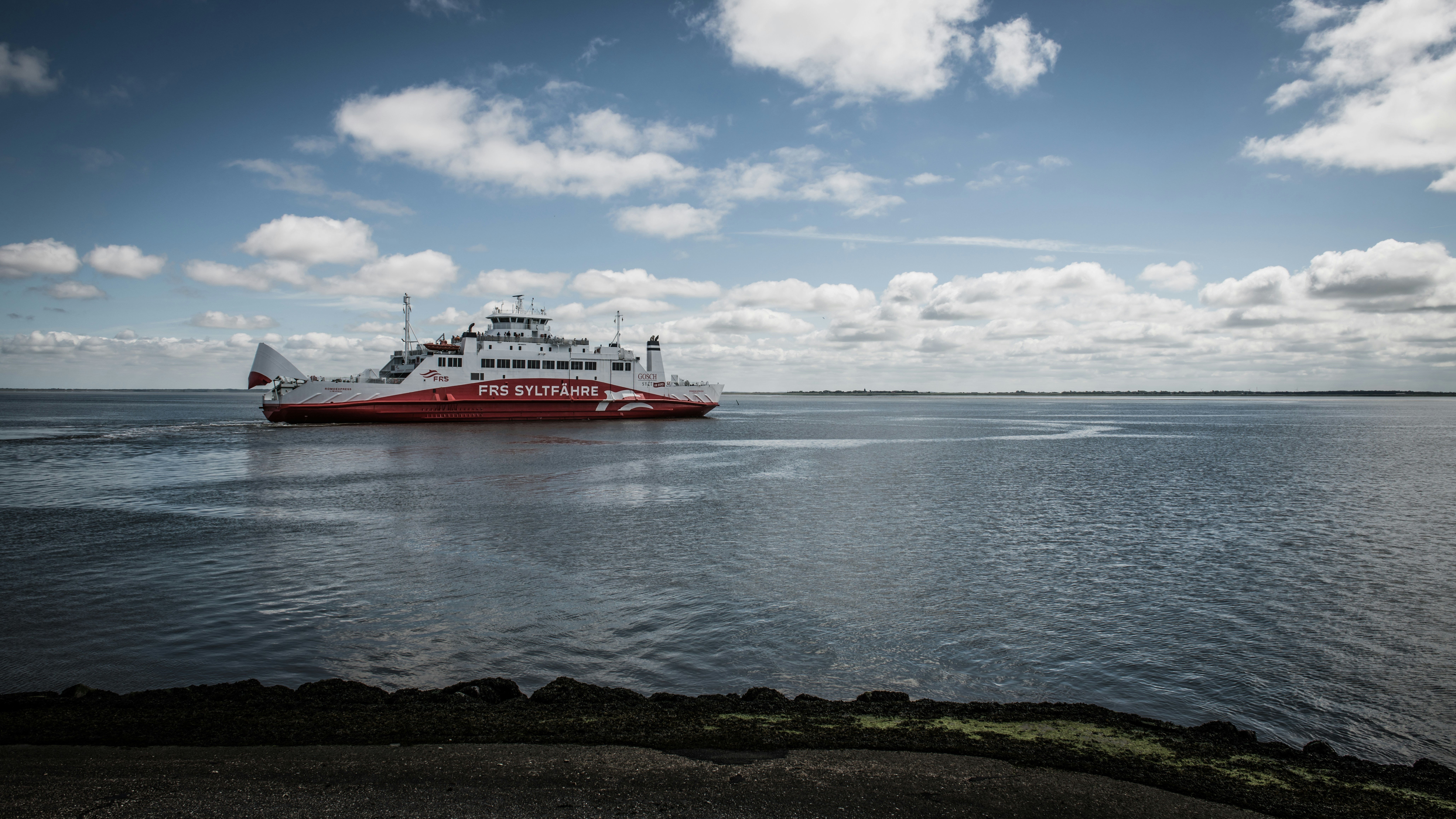 Red Ferry in a Quiet Harbor Beneath a Sky of Puffed Clouds