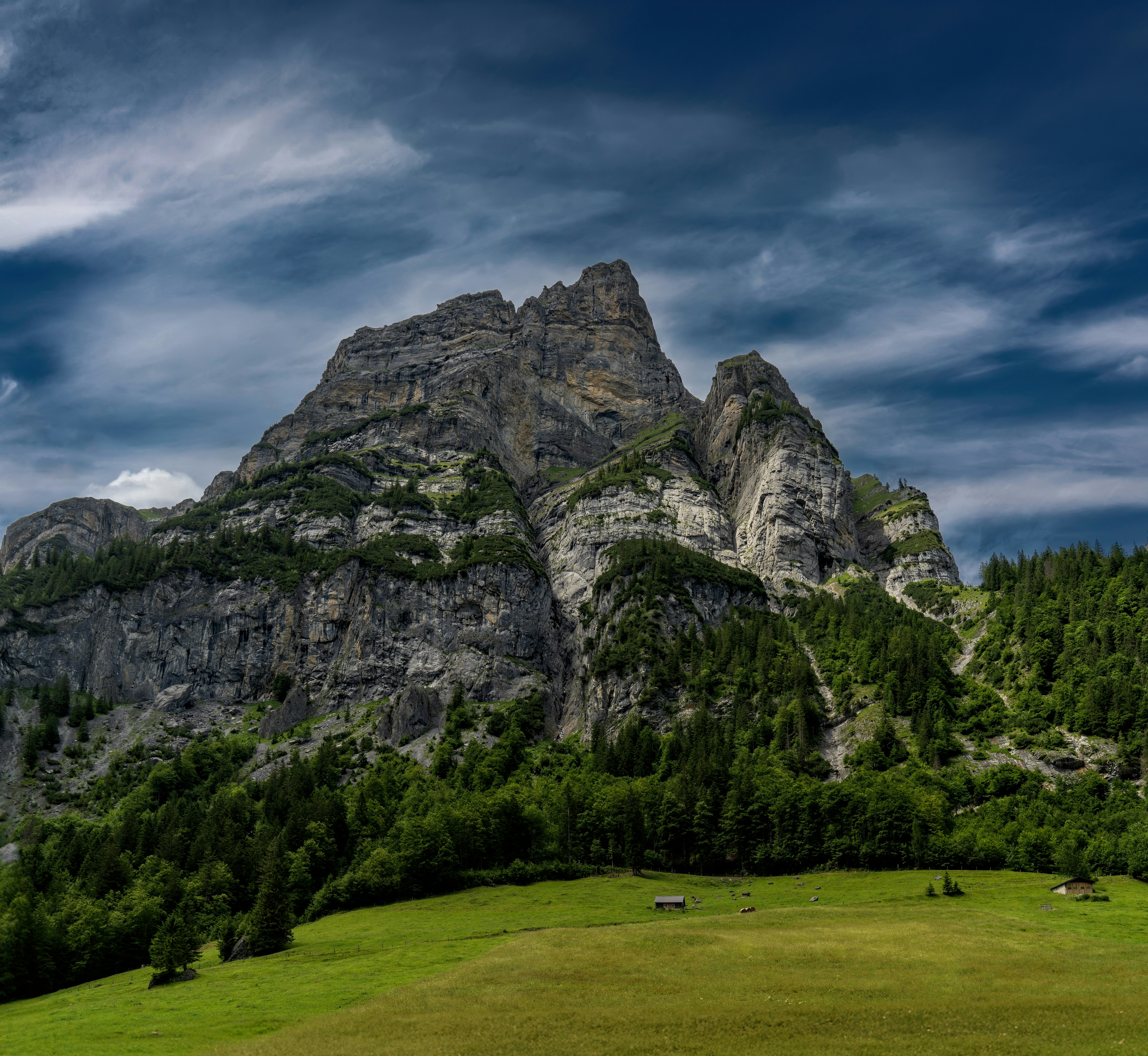 Towering mountain with rugged cliffs set against a dramatic sky and lush green foreground.