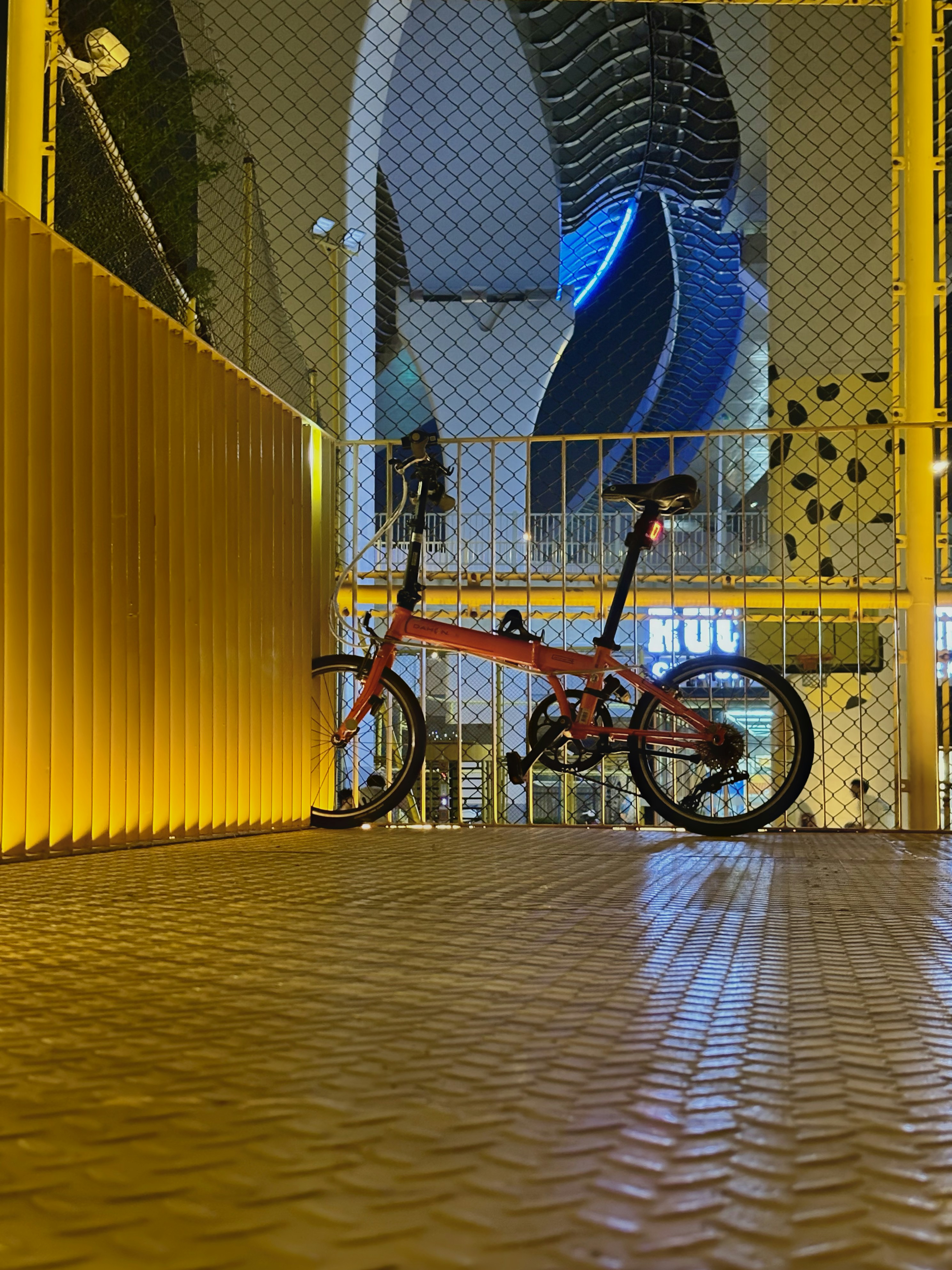 Red folding bicycle framed by a neon-yellow barrier under blue urban lighting