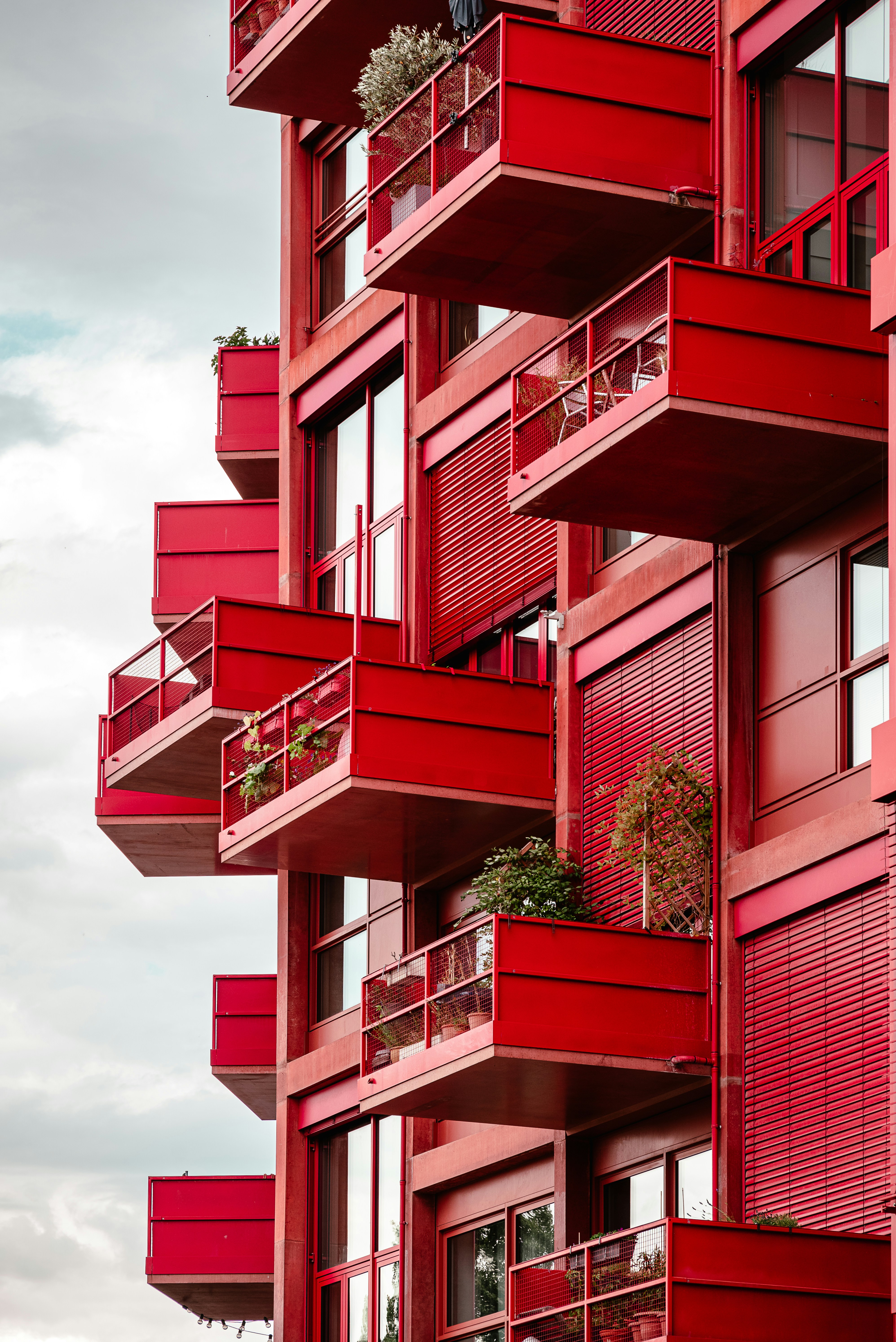 A tall red building with balconies and plants on the balconies photo ...