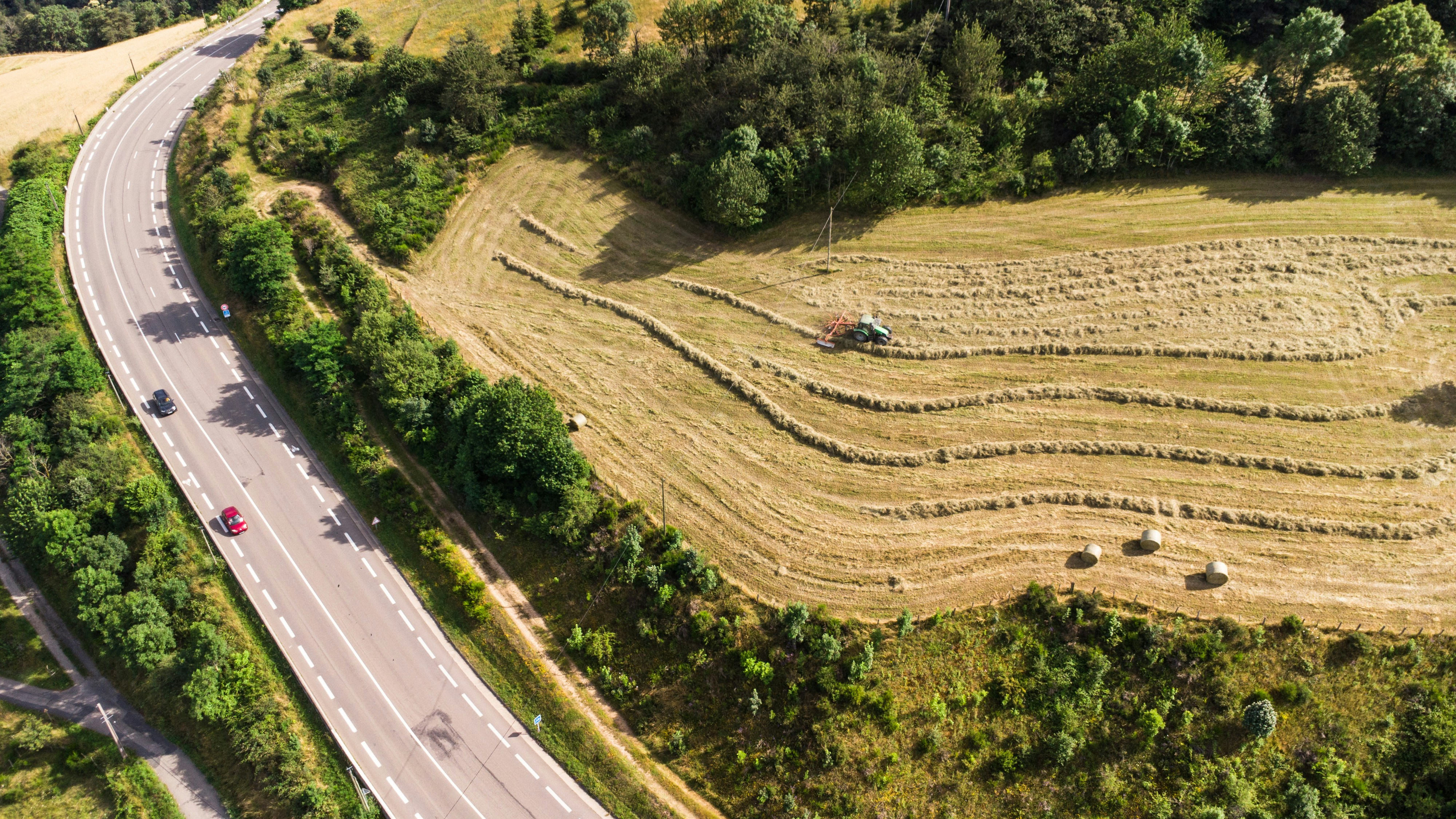 Aerial view of a curving road alongside neatly patterned fields and lush greenery.