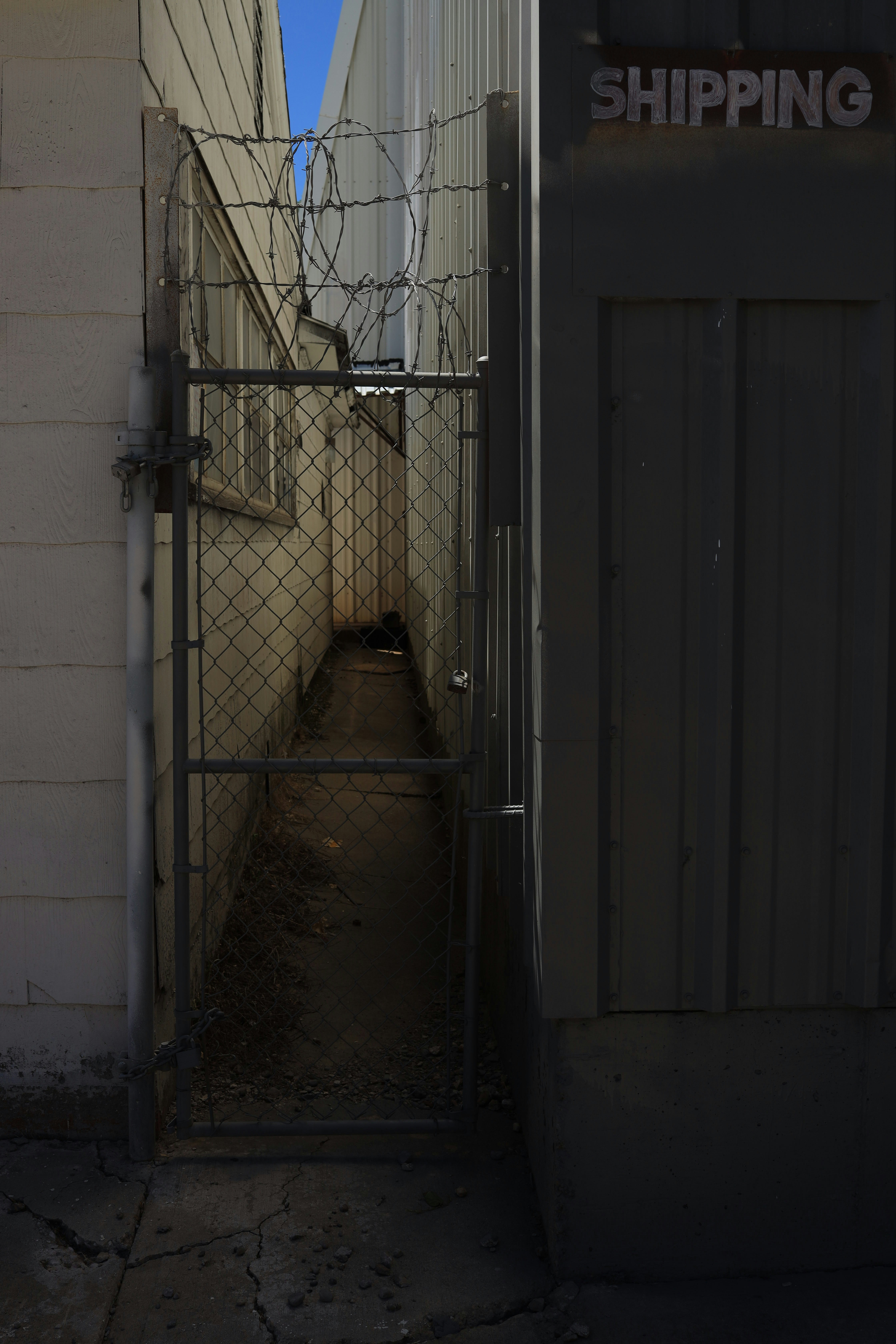 Shady chain link fence with barbed wire. Shipping | A narrow alley with a chain link fence