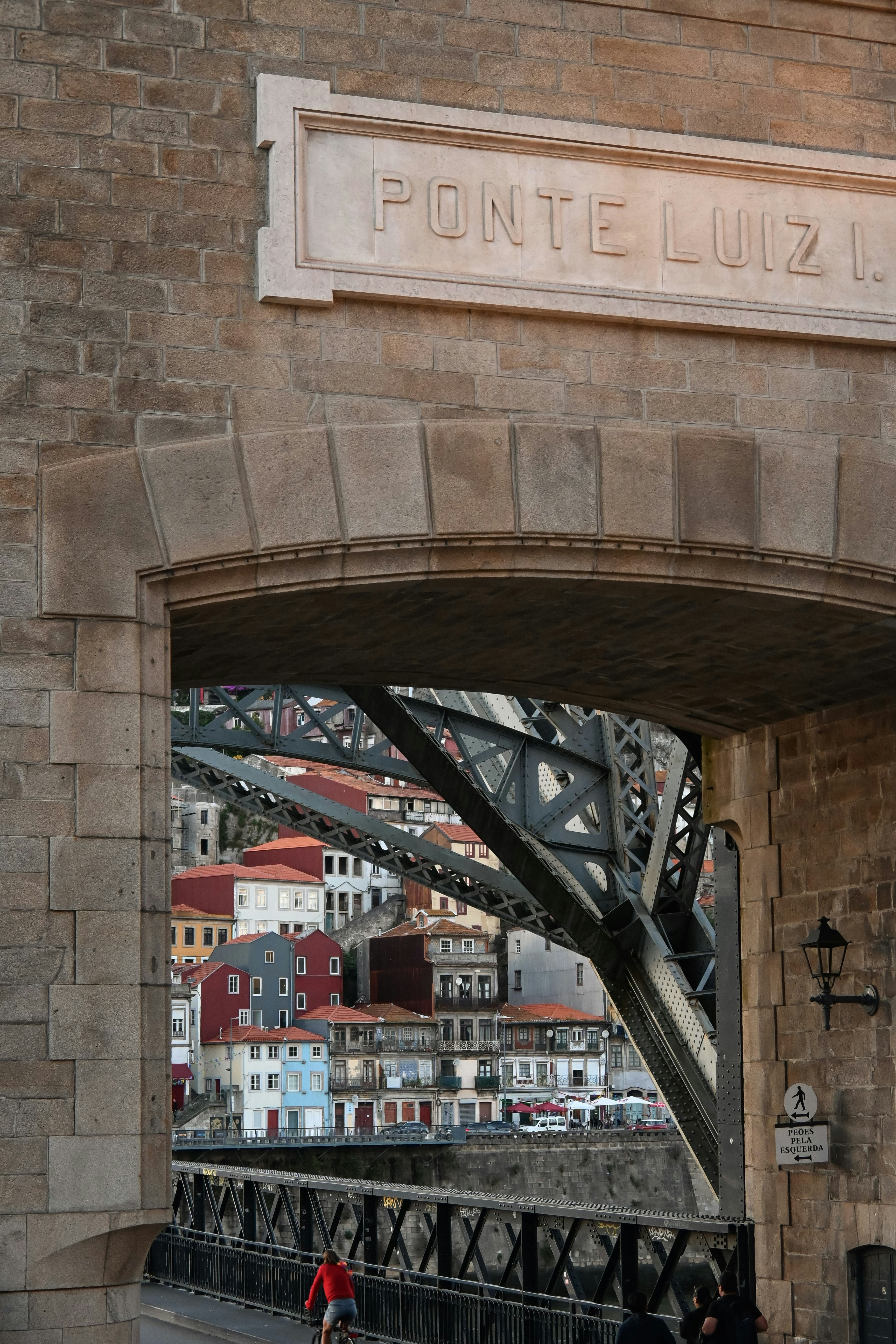 Under Ponte Luís I's Arch: Red-Clad Pedestrian Framed by Porto's Colorful Douro Quarter