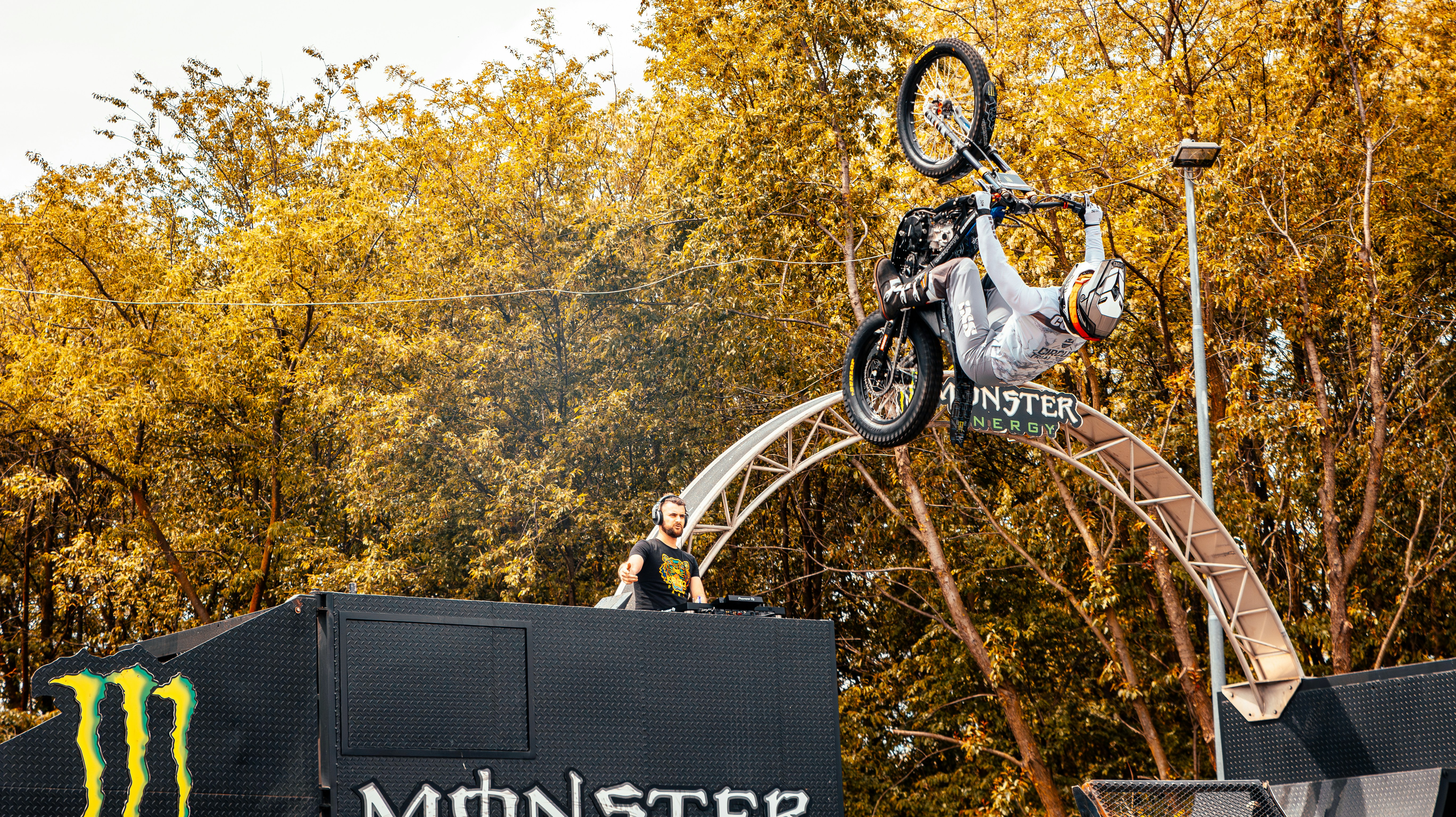Motorcycle performs an aerial stunt over a ramp framed by autumn trees.