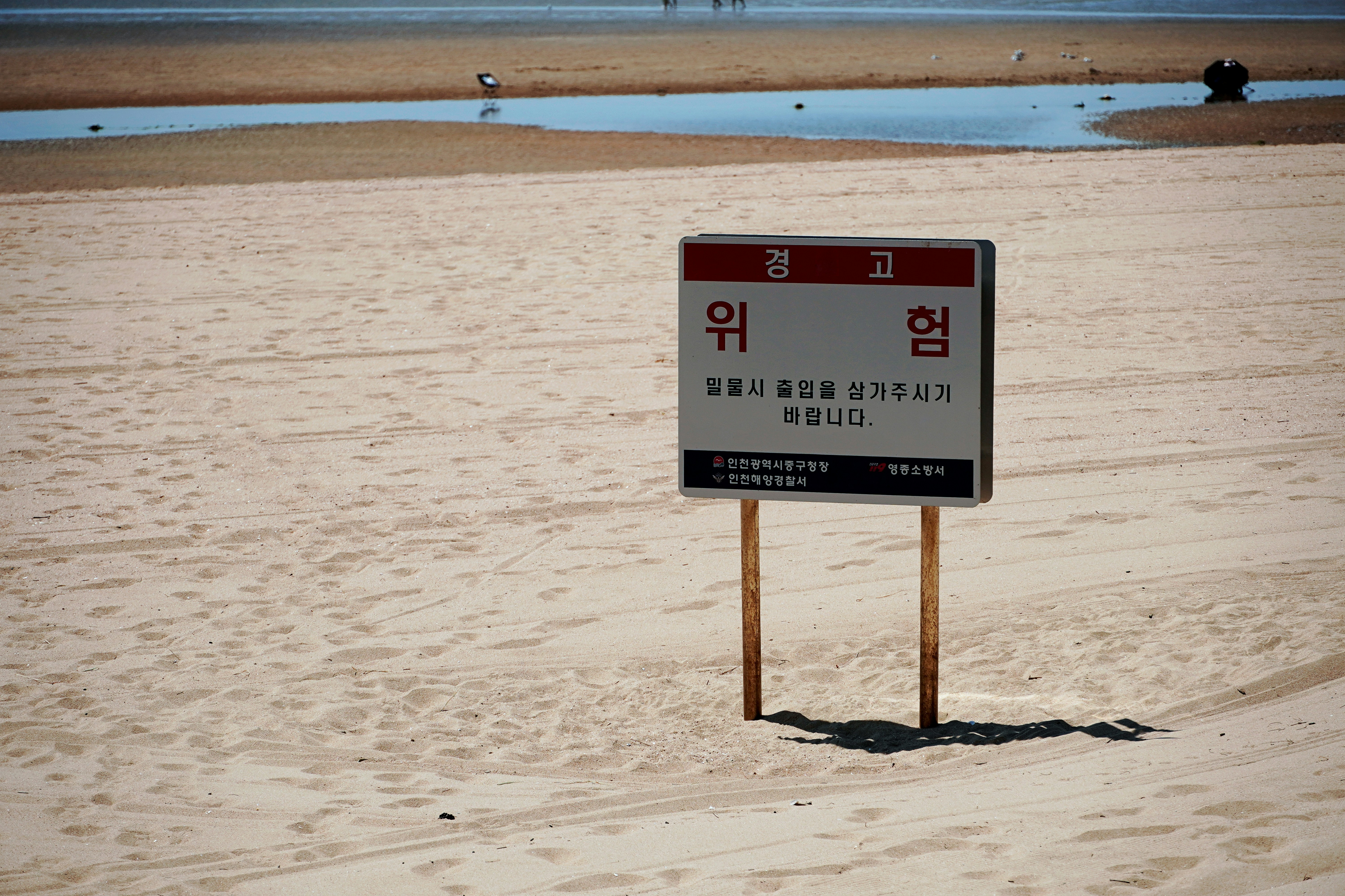 Lone warning sign on a sunlit beach stands against the distant tide