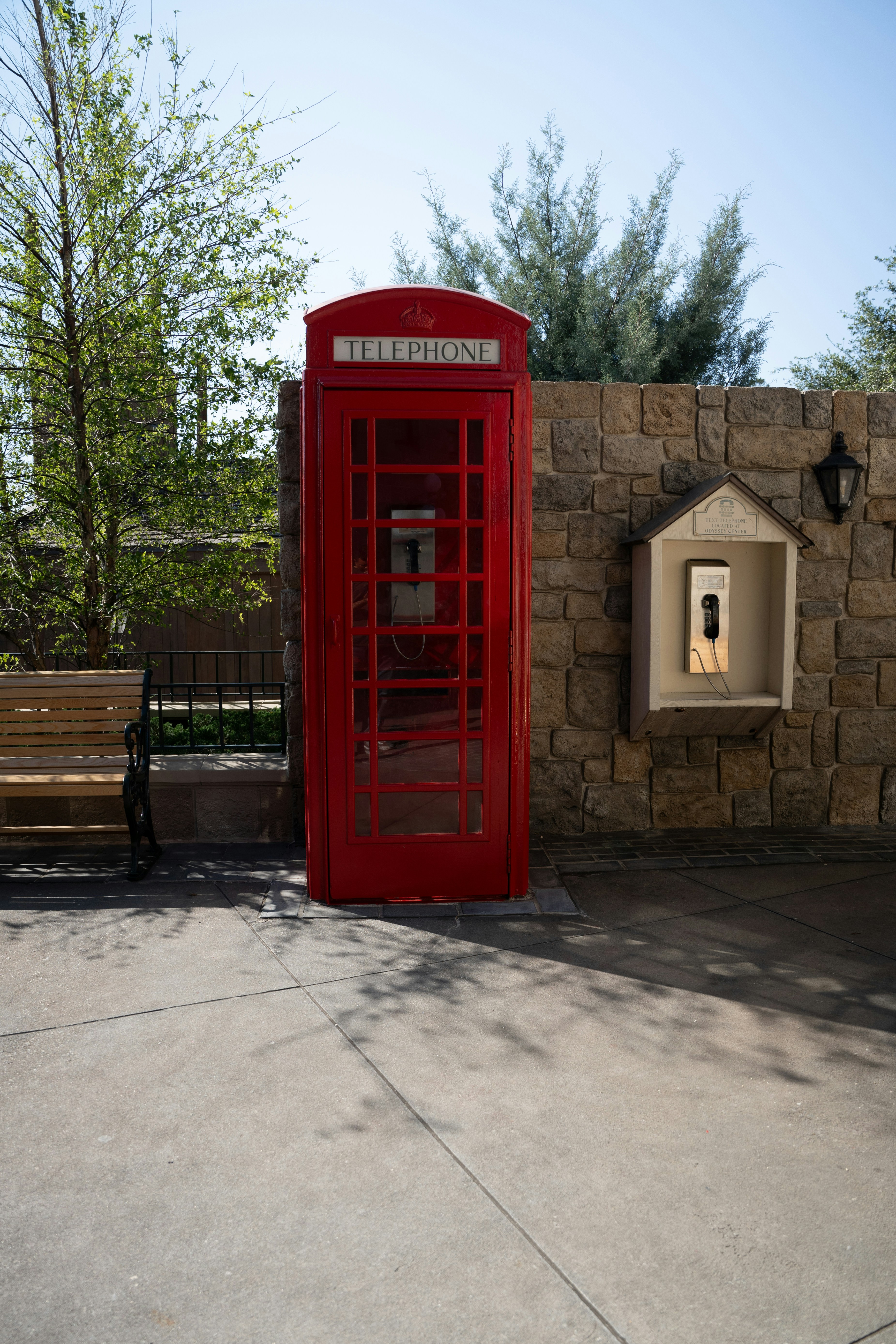 Crimson Call: A Red Telephone Booth Anchoring a Sunlit Stone Wall