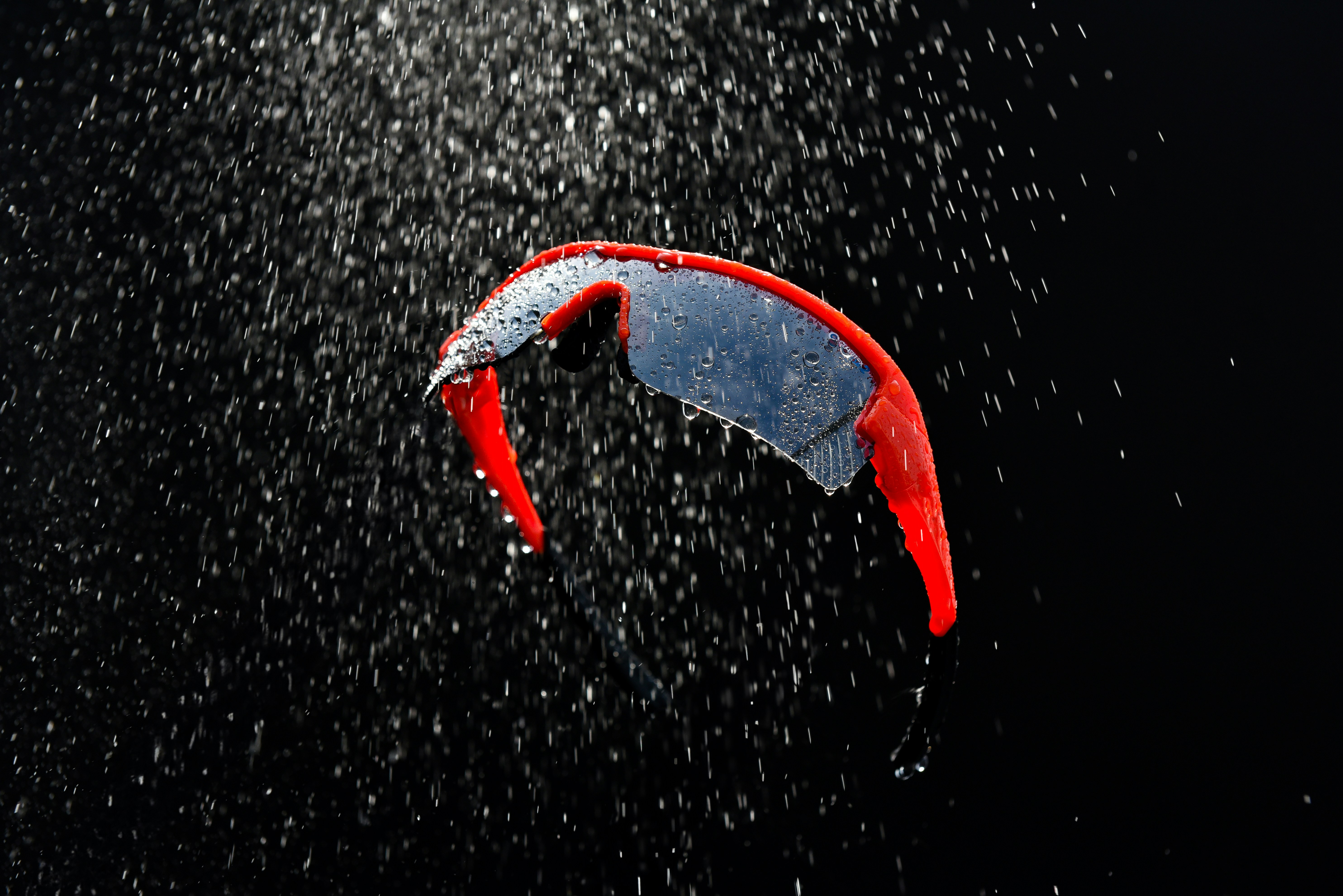 Red wing-like object captured mid-splash against dark backdrop, droplets surrounding it, emphasizing motion and micro-texture of rain.