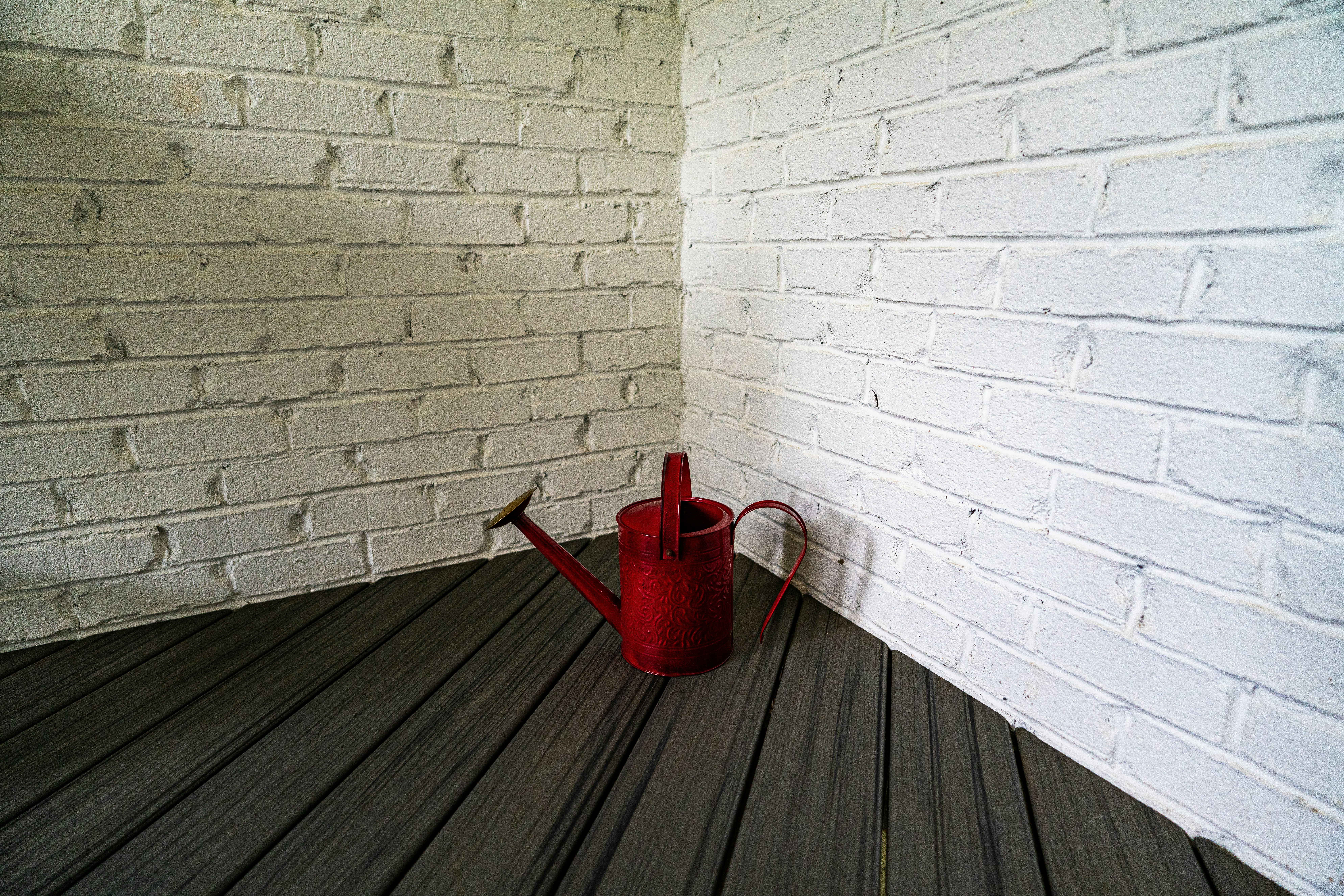 Red watering pot positioned against white brick wall.