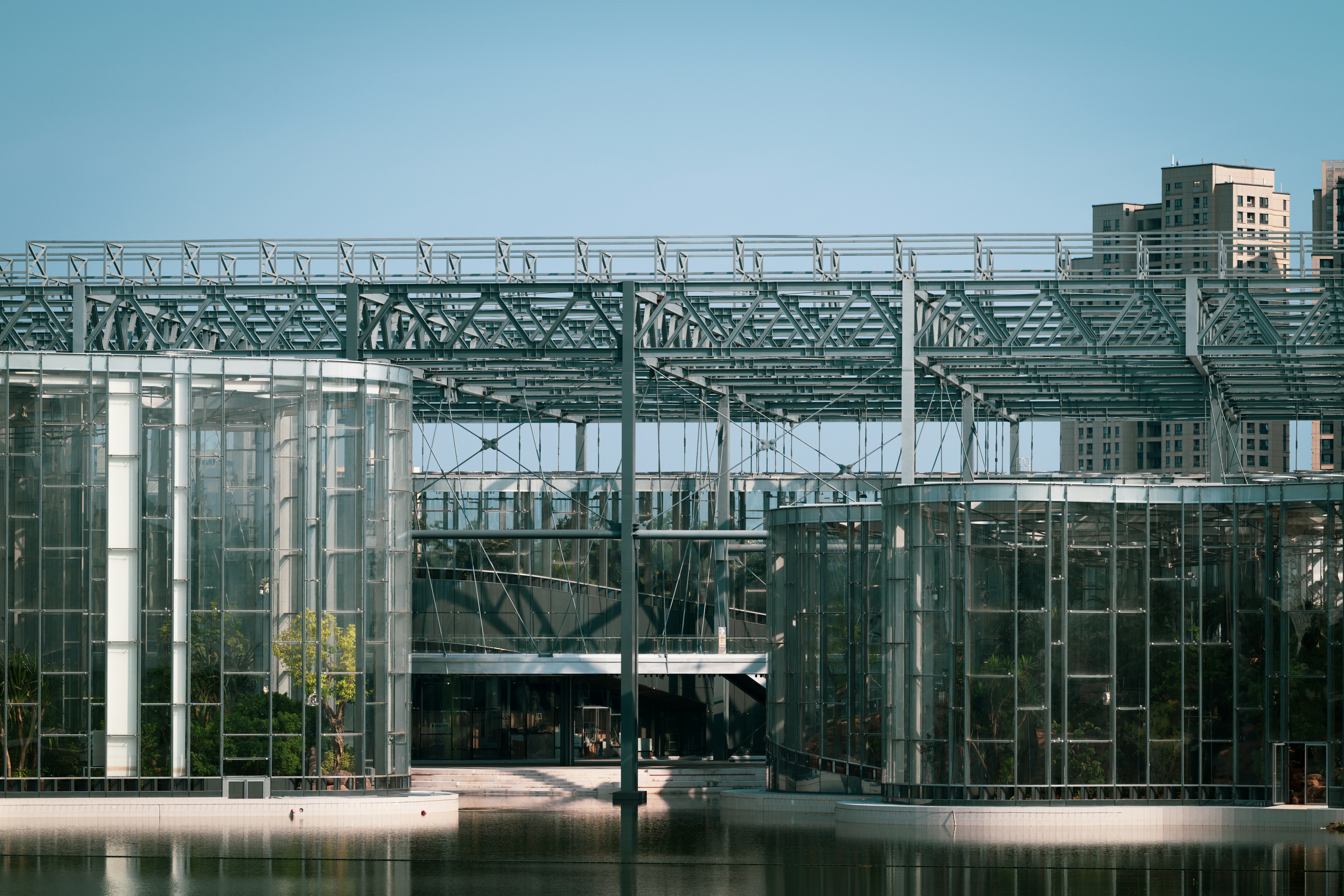 Glass Atrium Over Water: Framed by Steel Lattices and Skyline