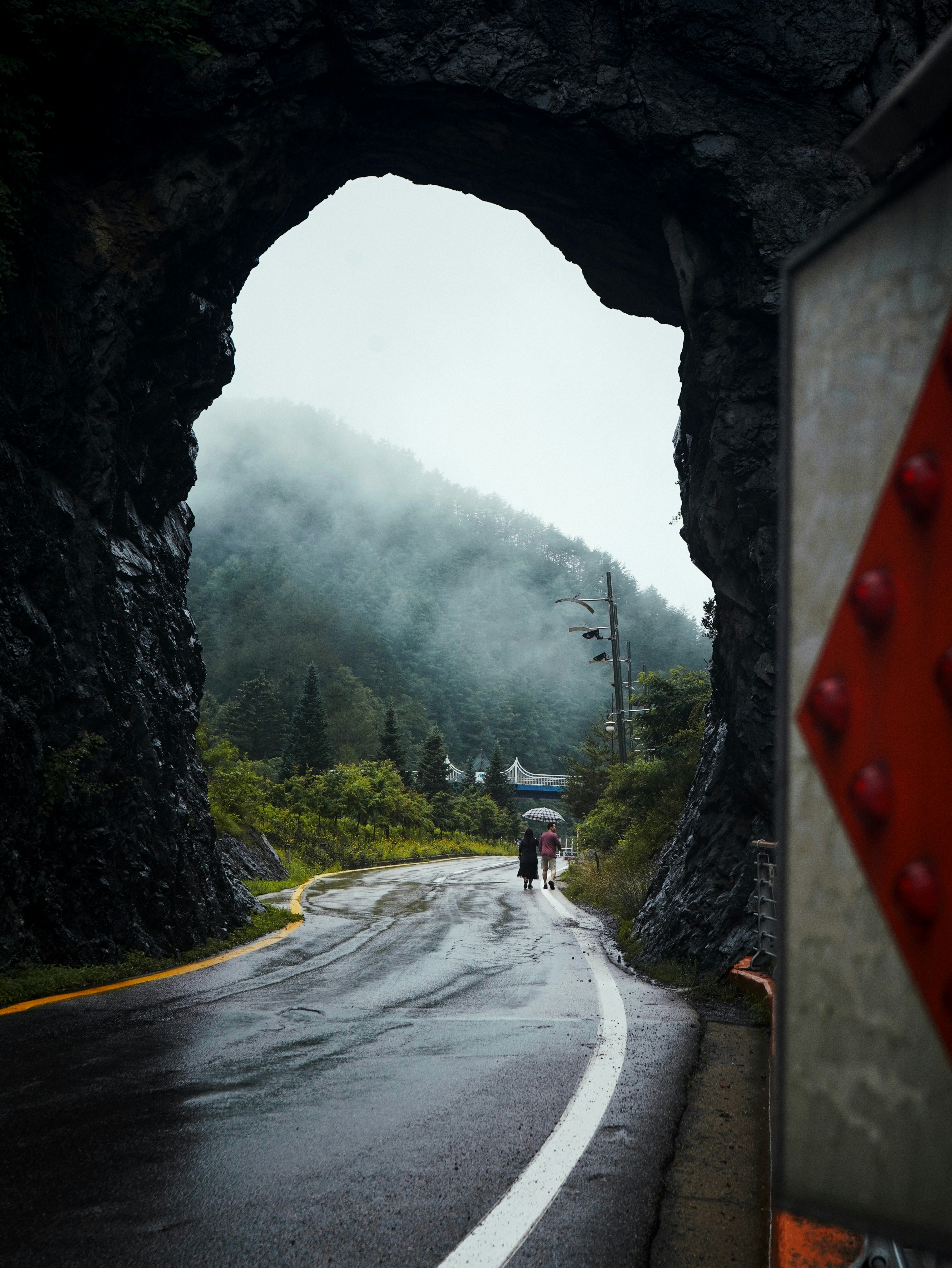 Mist-veiled Gateway: Pedestrians Beneath a Stone Arch on a Rain-Washed Road