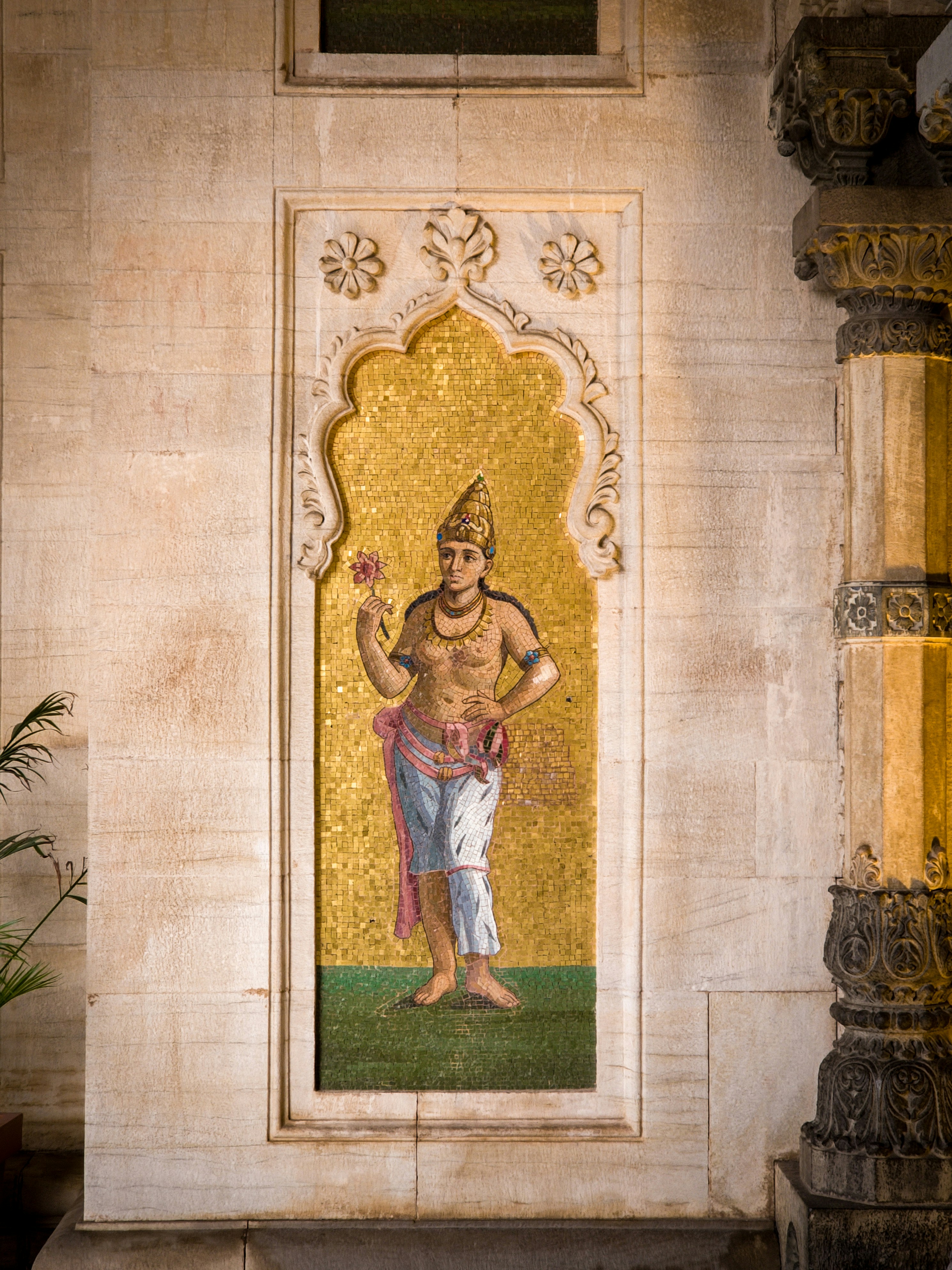 Golden mosaic mural of a dancing figure framed by a carved temple niche in a stone wall.