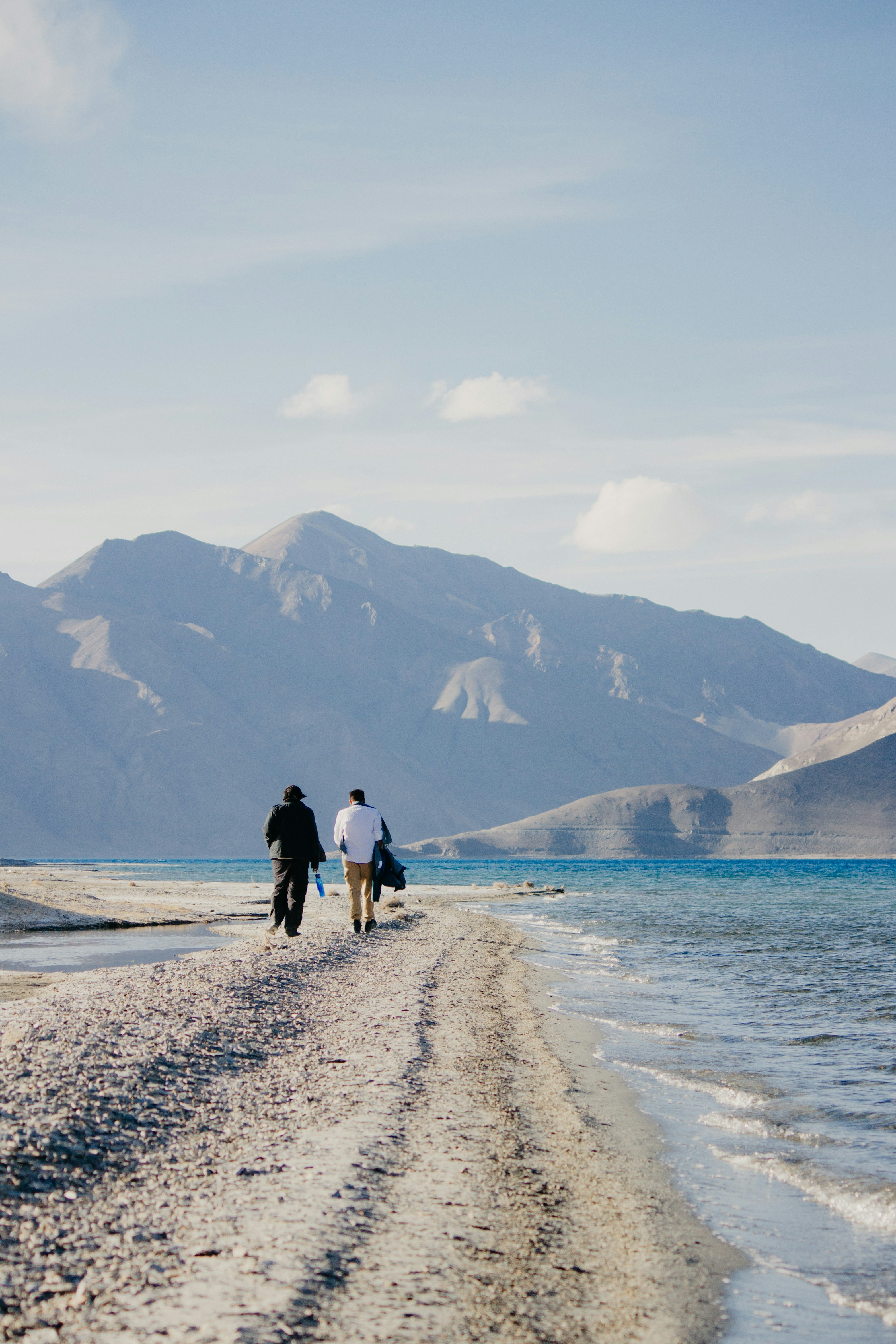 Two people walking on a beach with mountains in the background photo ...