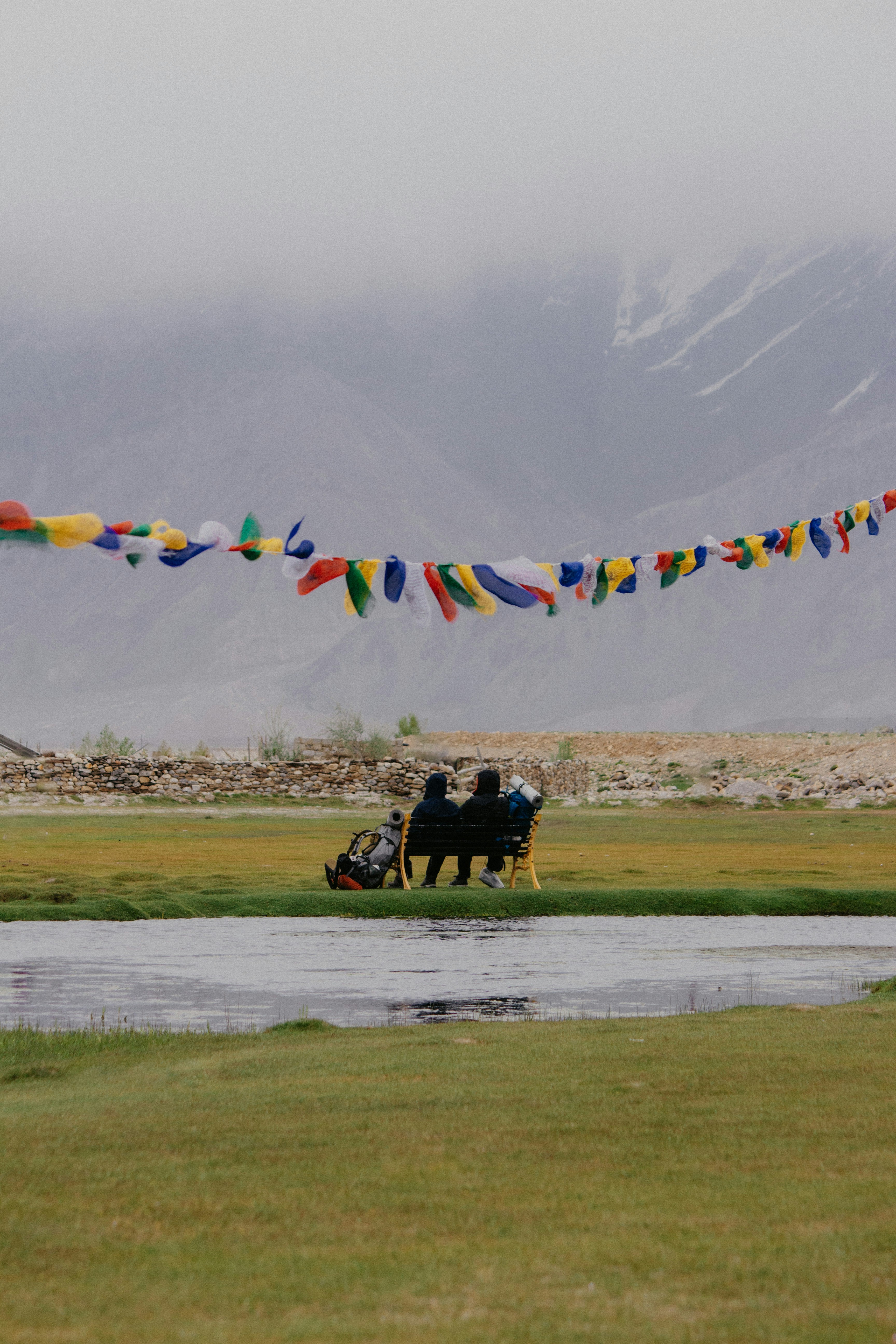 Benchside Moment Under Colorful Prayer Flags With Snowy Valley Backdrop