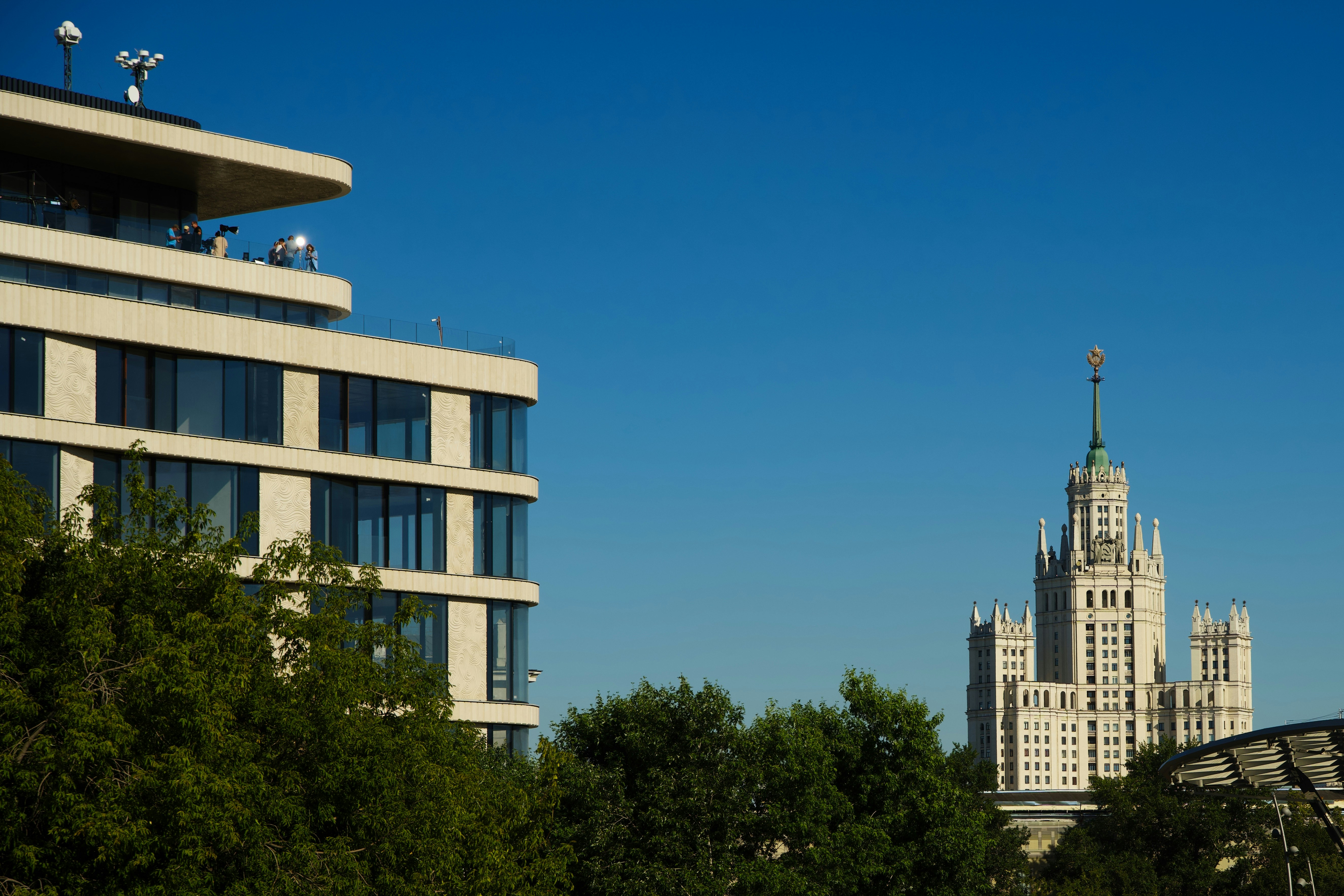 Contemporary building juxtaposed with a historic skyscraper under a clear blue sky.