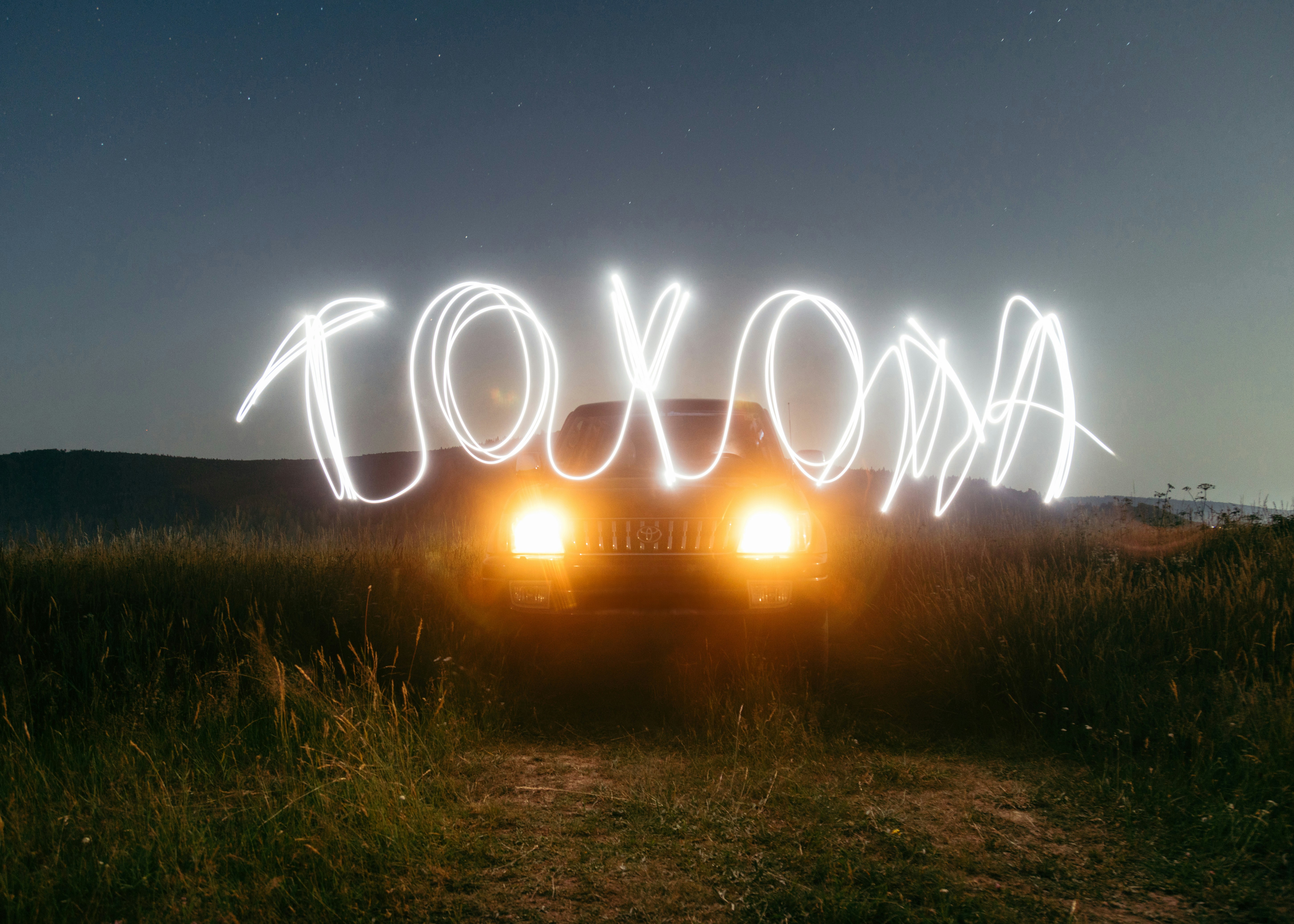 Neon Script over a Midnight Field: The Car’s Headlights Trace a Light-Painted Word